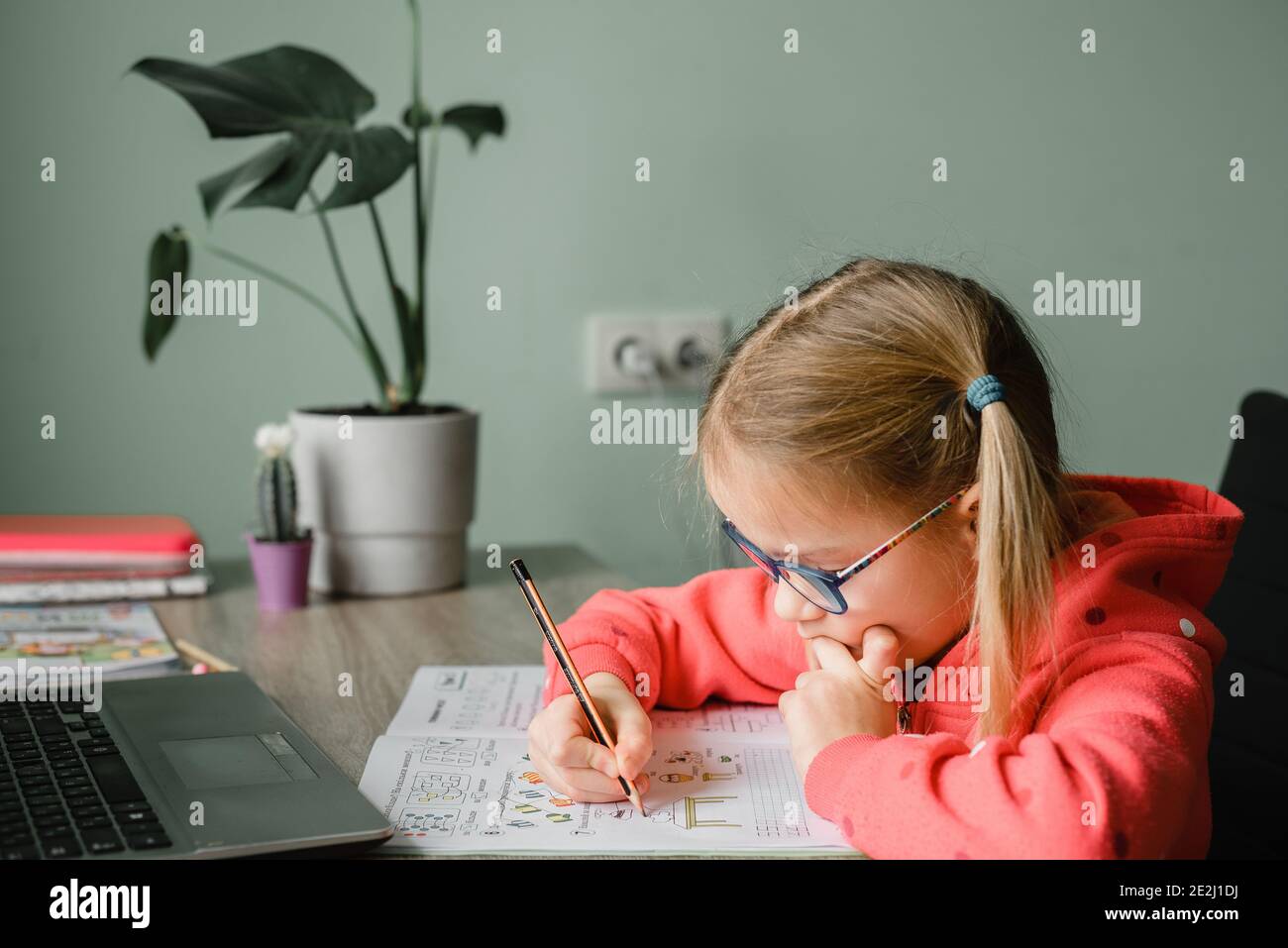 Junior student girl in eyelgasses writing in her notebook whily ...