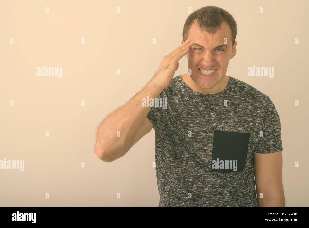 Studio shot of angry young muscular man having headache against white ...