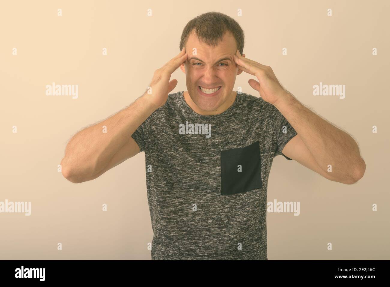 Studio shot of angry young muscular man having headache with both hands ...