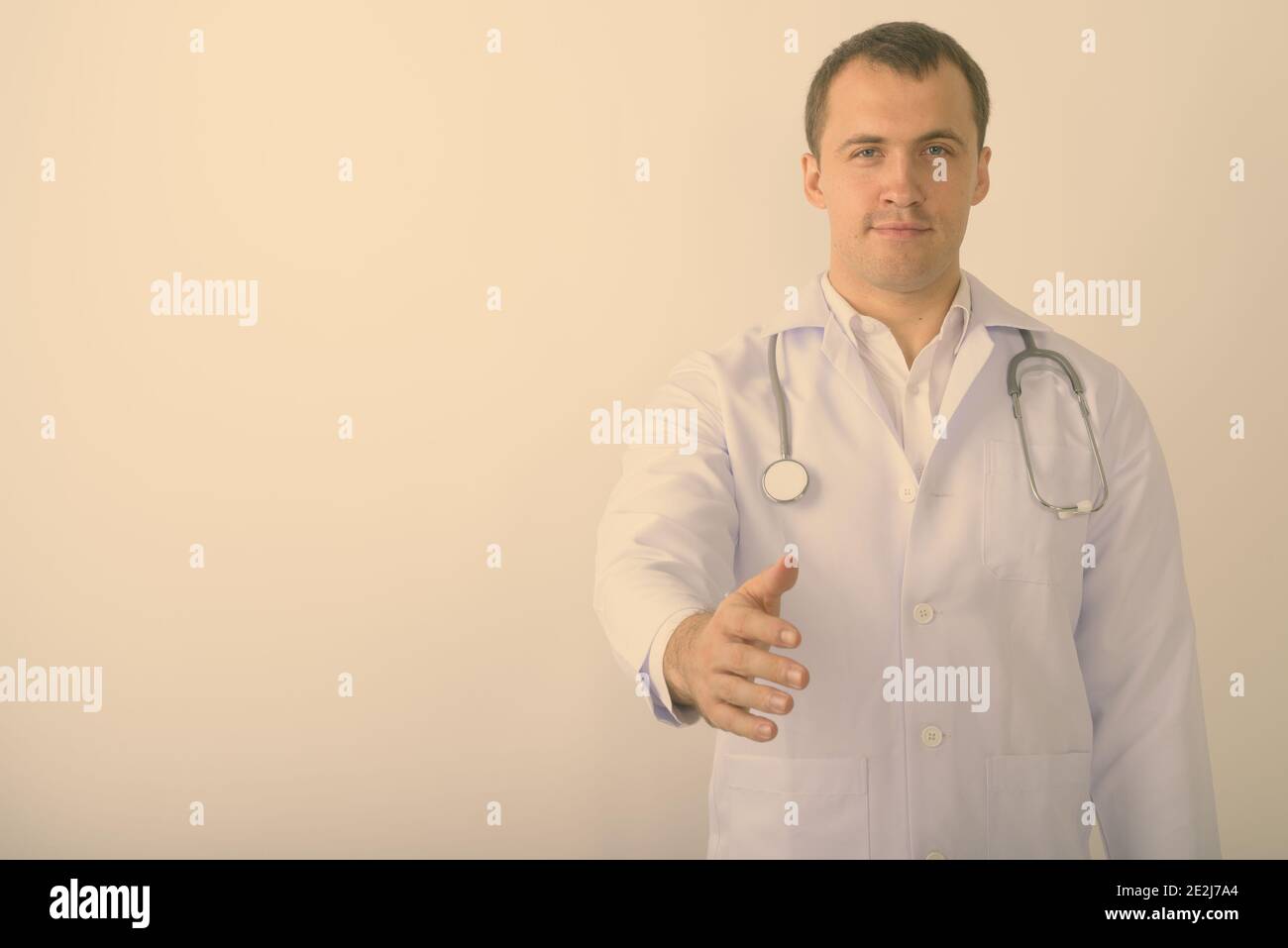 Studio shot of young muscular man doctor giving handshake against white ...