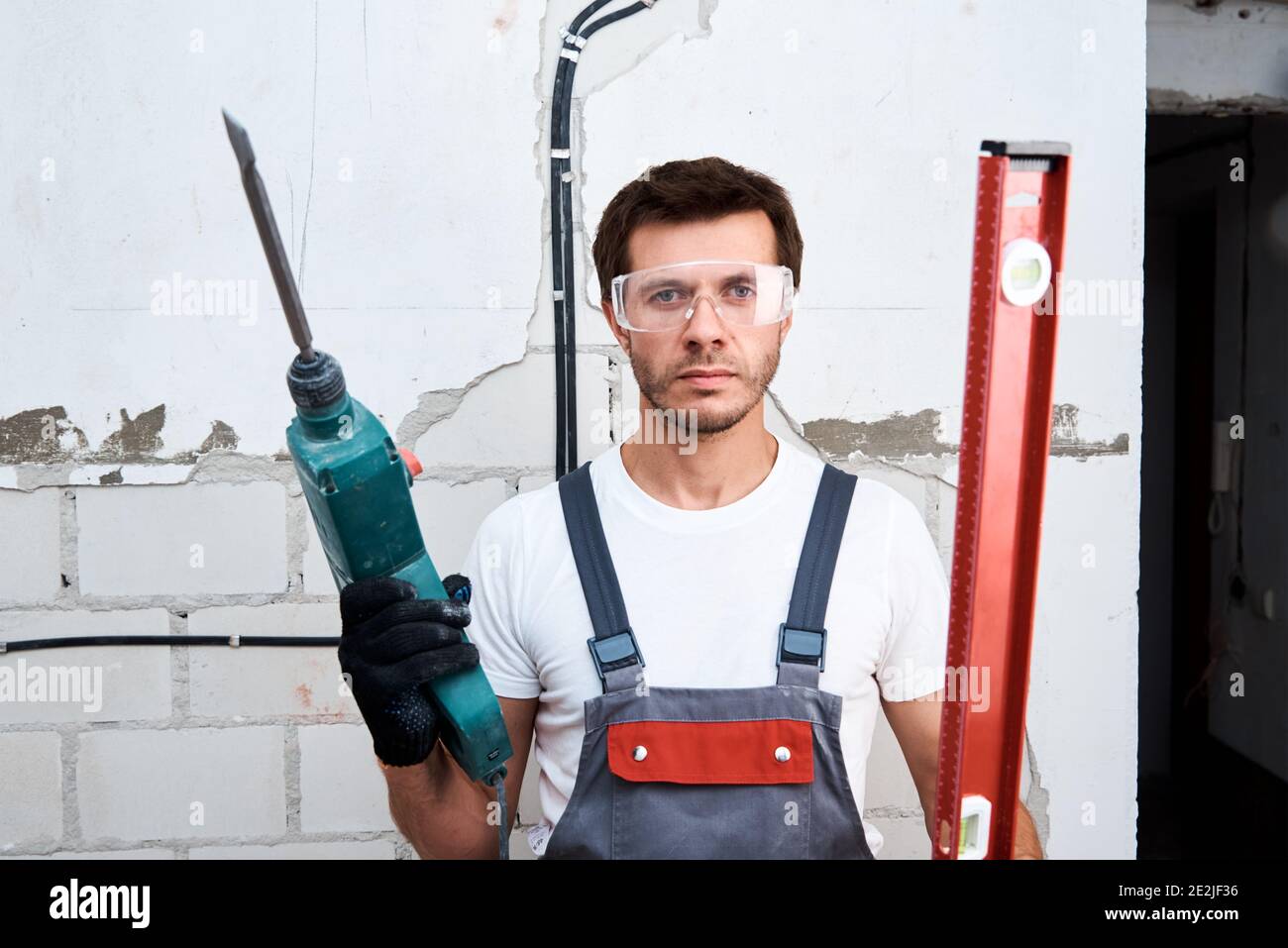 Worker man with a hammer drill and building level at construction site ...
