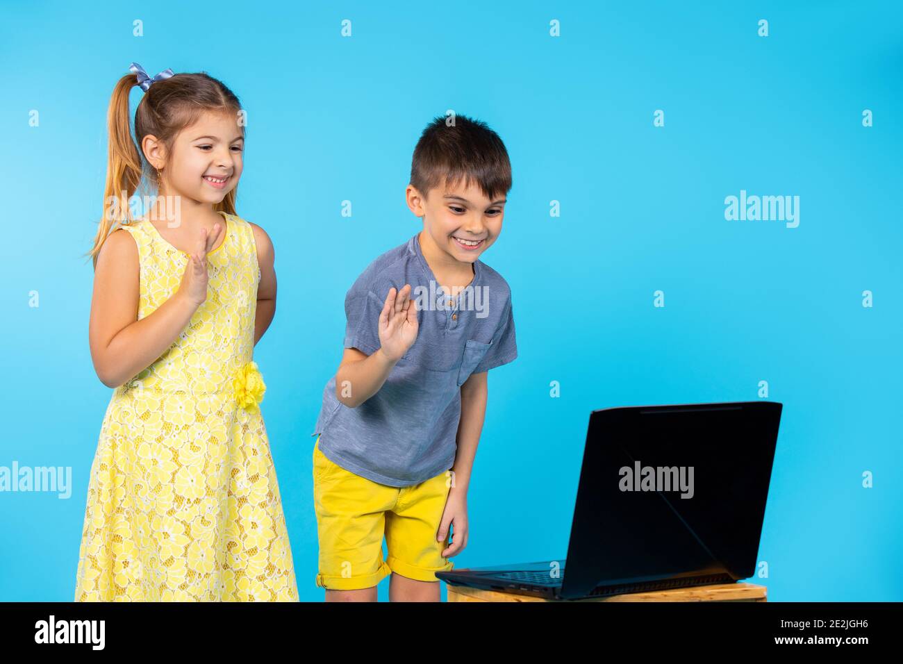Preschool children communicate by video call via laptop and waving hand ...