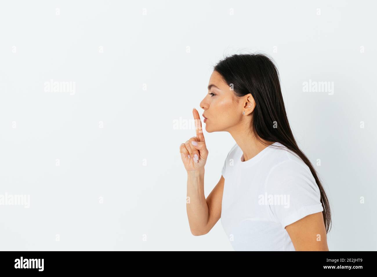 Attractive brunette woman holding index finger near lips on white ...