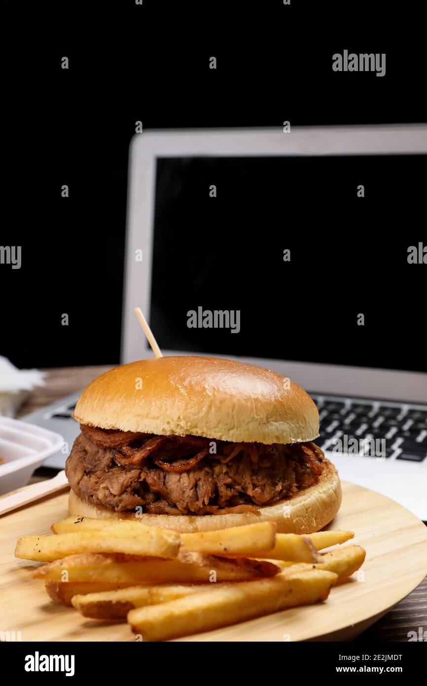 Fresh cooked beef burger with french fries in front of laptop against ...