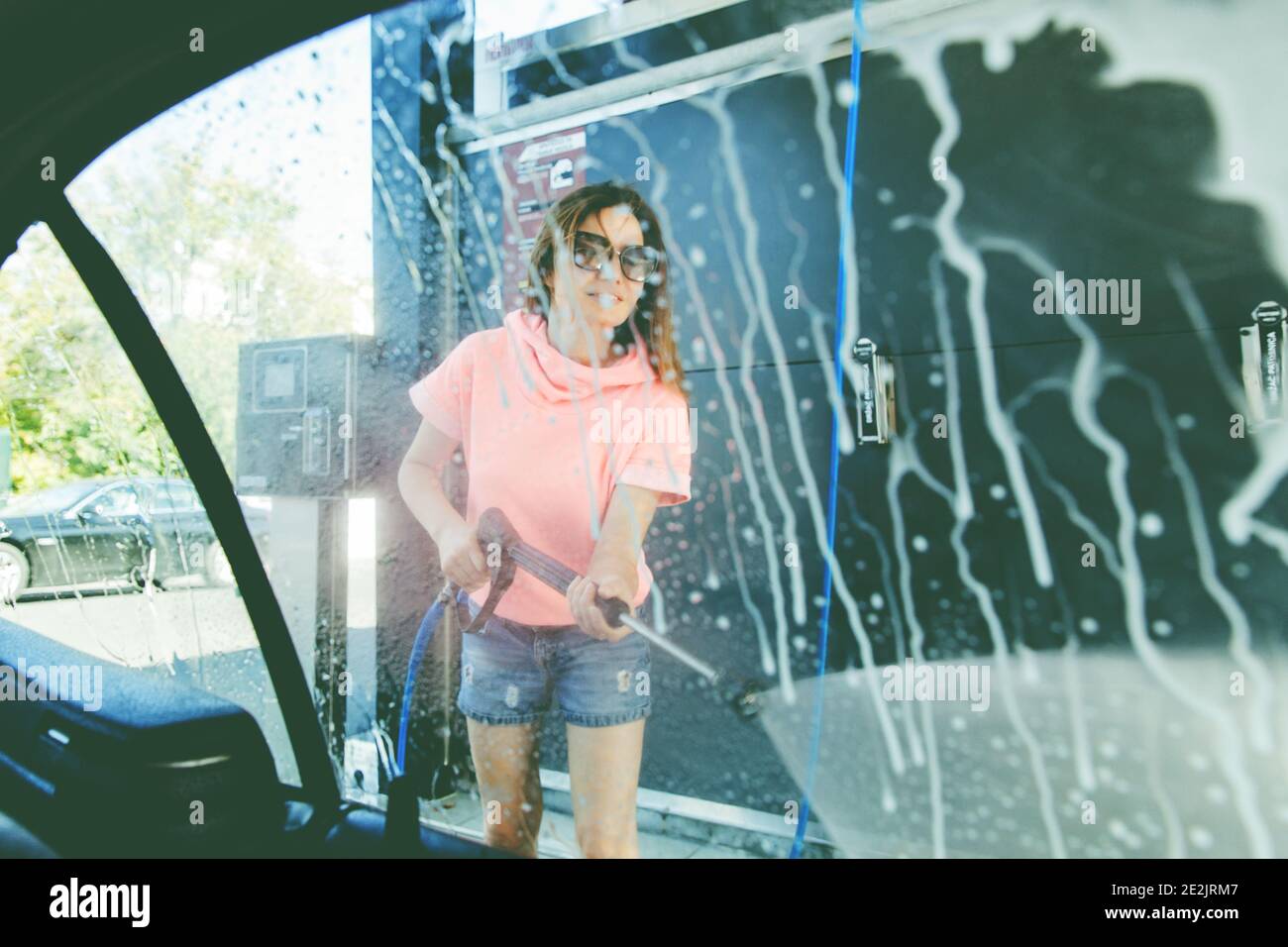 Woman washing her car with high pressure sprayer at self-serve car wash ...