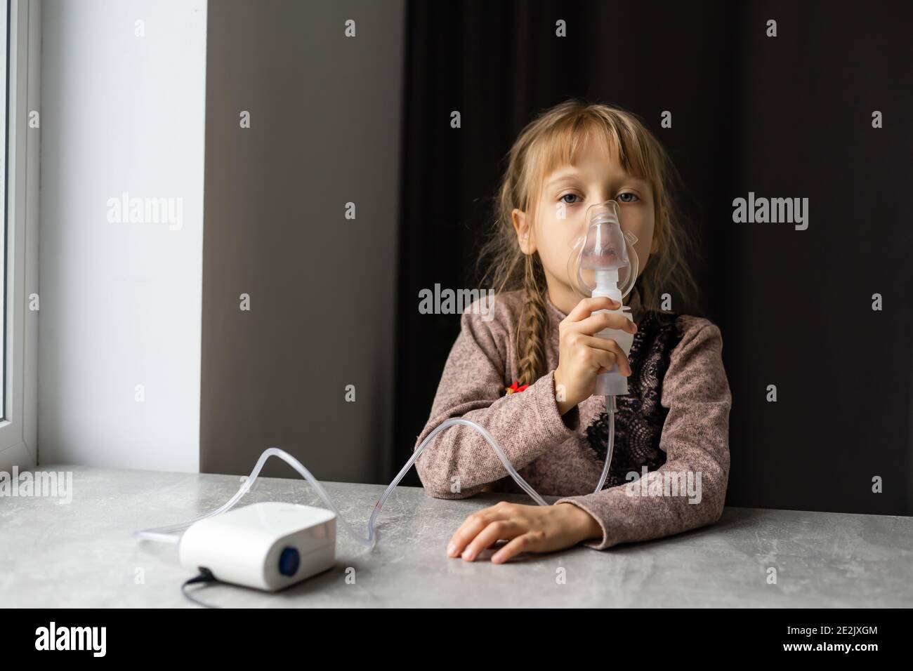 Little girl makes inhalation with a nebulizer at home, sitting on a ...
