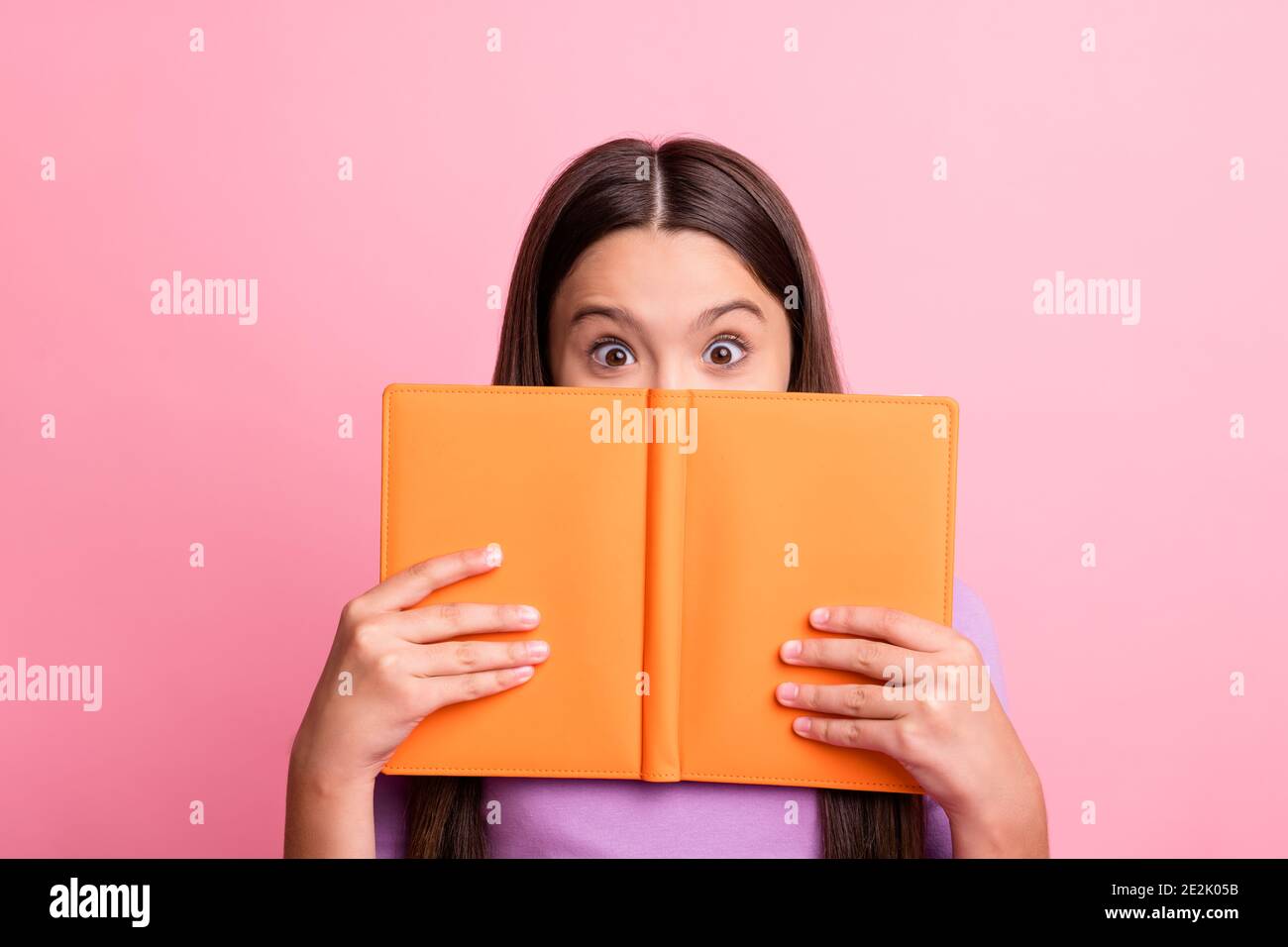 Photo of excited impressed kid girl hide her lips with book wear violet ...