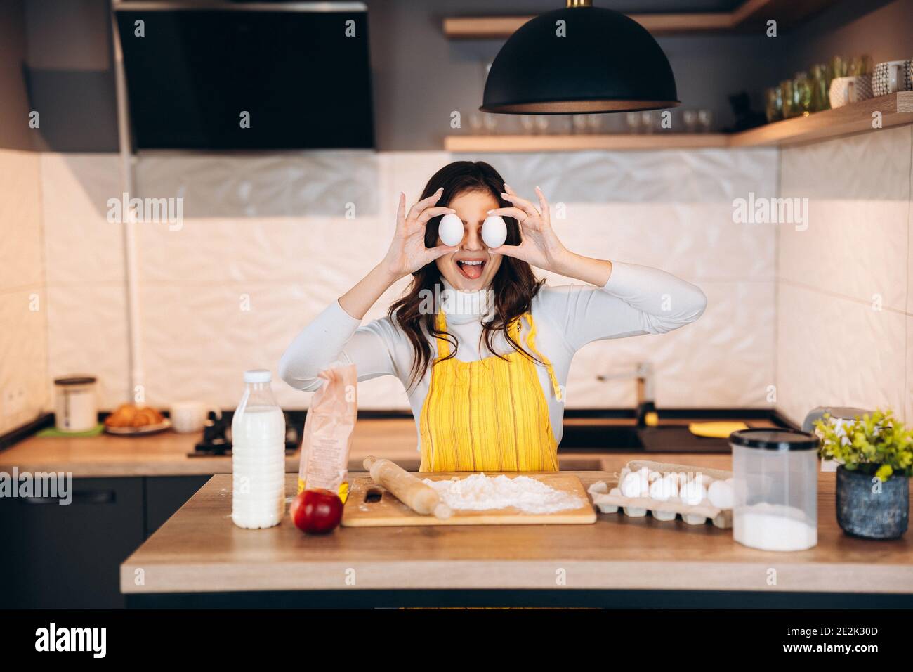 Young woman is covering her eyes by eggs while cooking in the kitchen ...