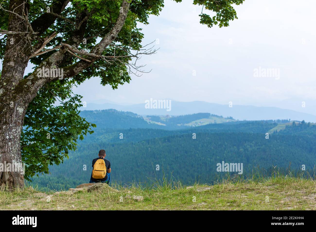 Alone guy sitting on cliff and enjoy peaceful green mountains landscape ...