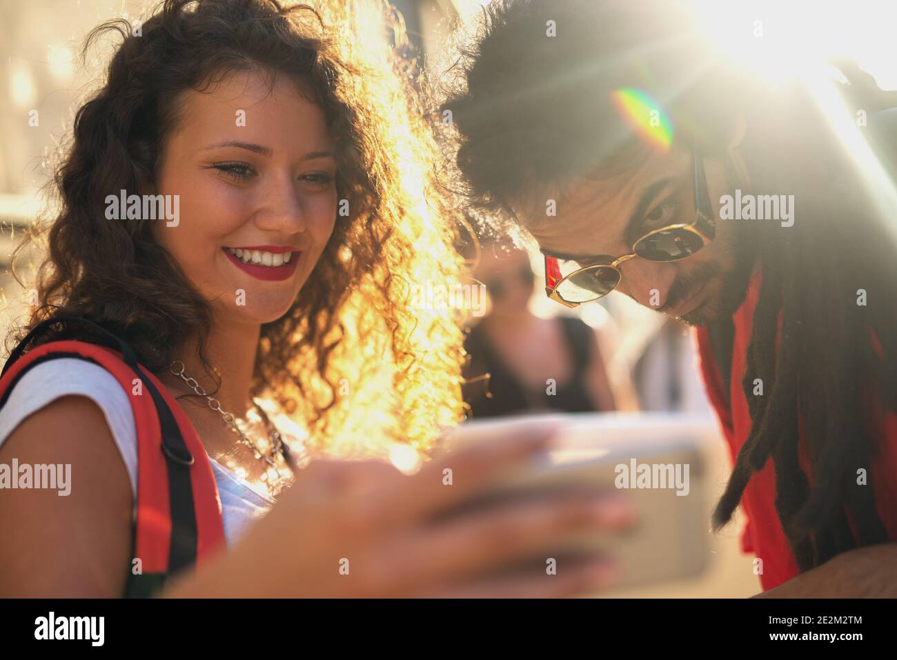 Beautiful happy curly girl is showing her boyfriend content on her phone that made him very ...