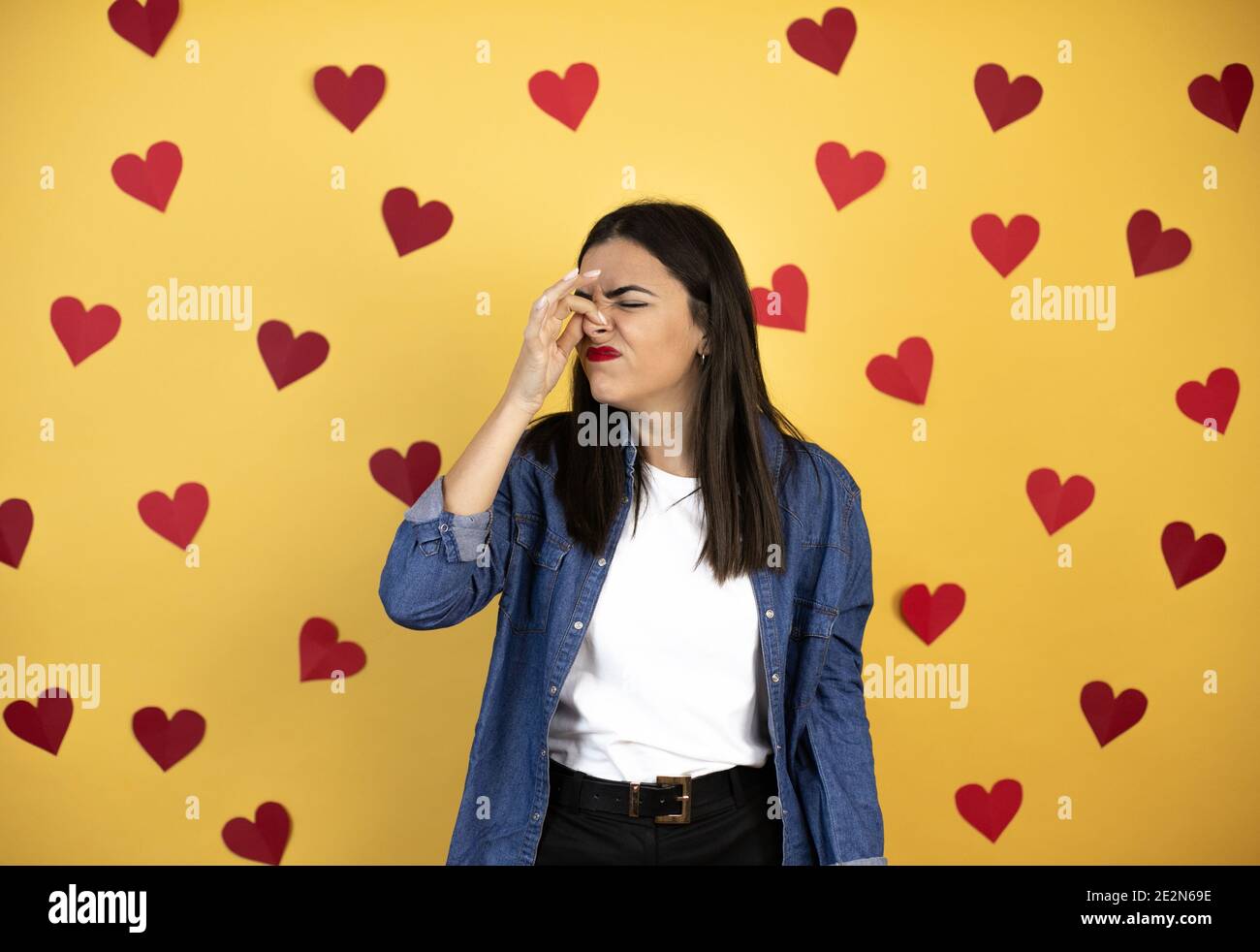 Young caucasian woman over yellow background with red hearts smelling ...