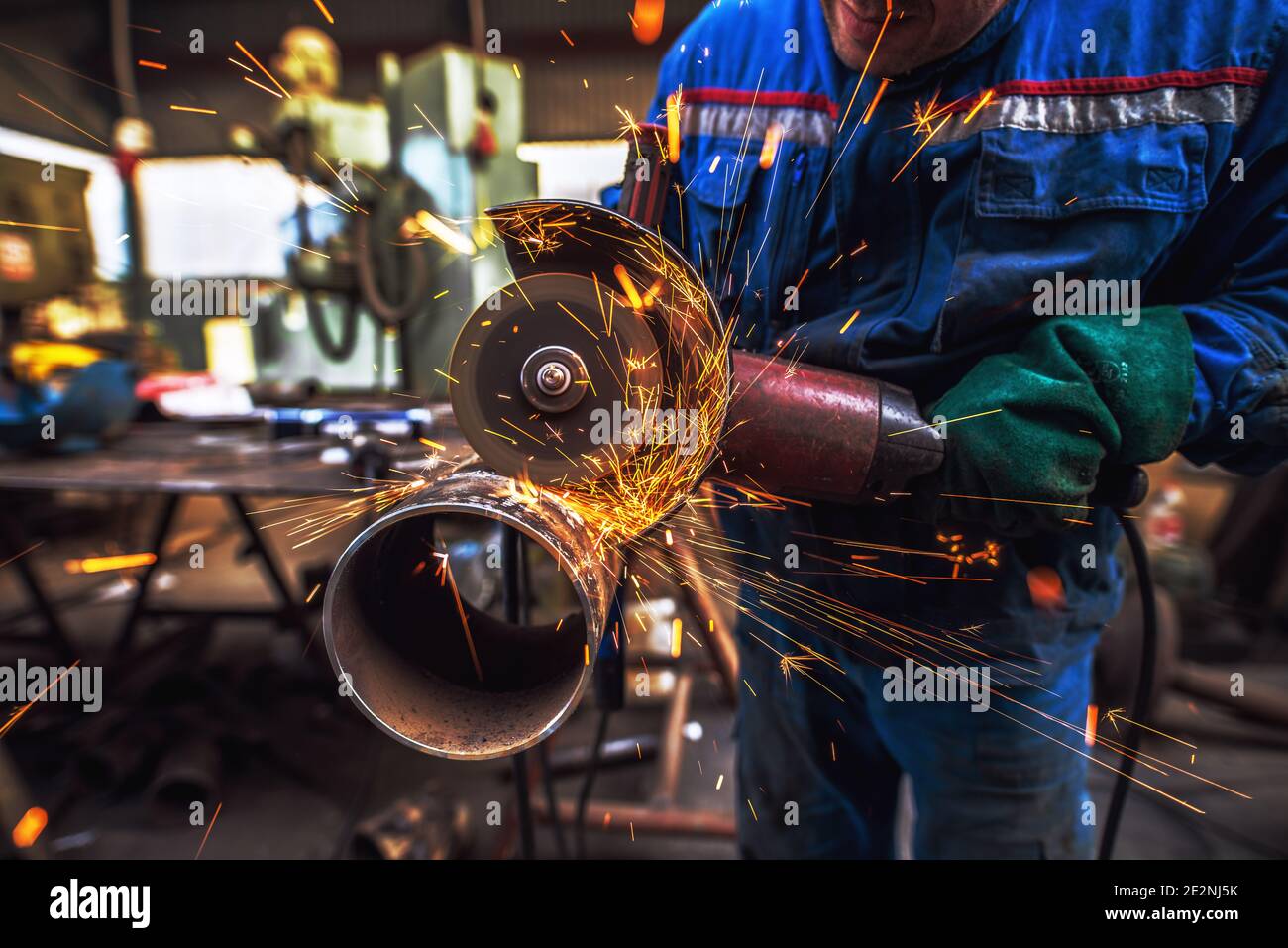 Male fabric worker cutting metal pipe with an electric grinder in ...