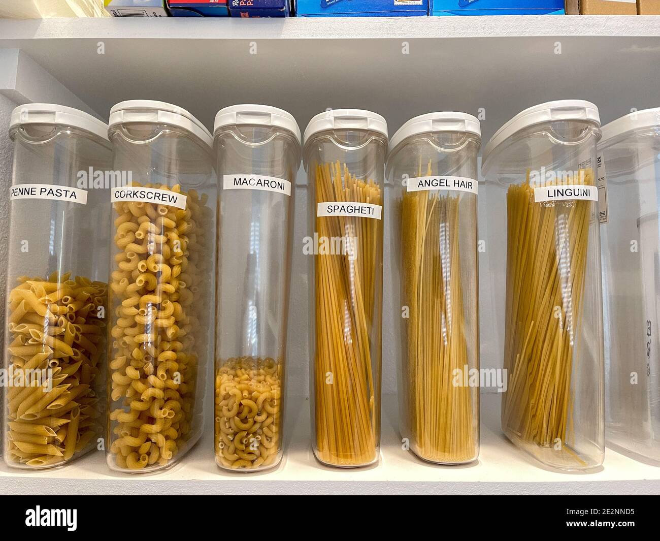 An organized pantry shelf with various types of pasta in plastic ...