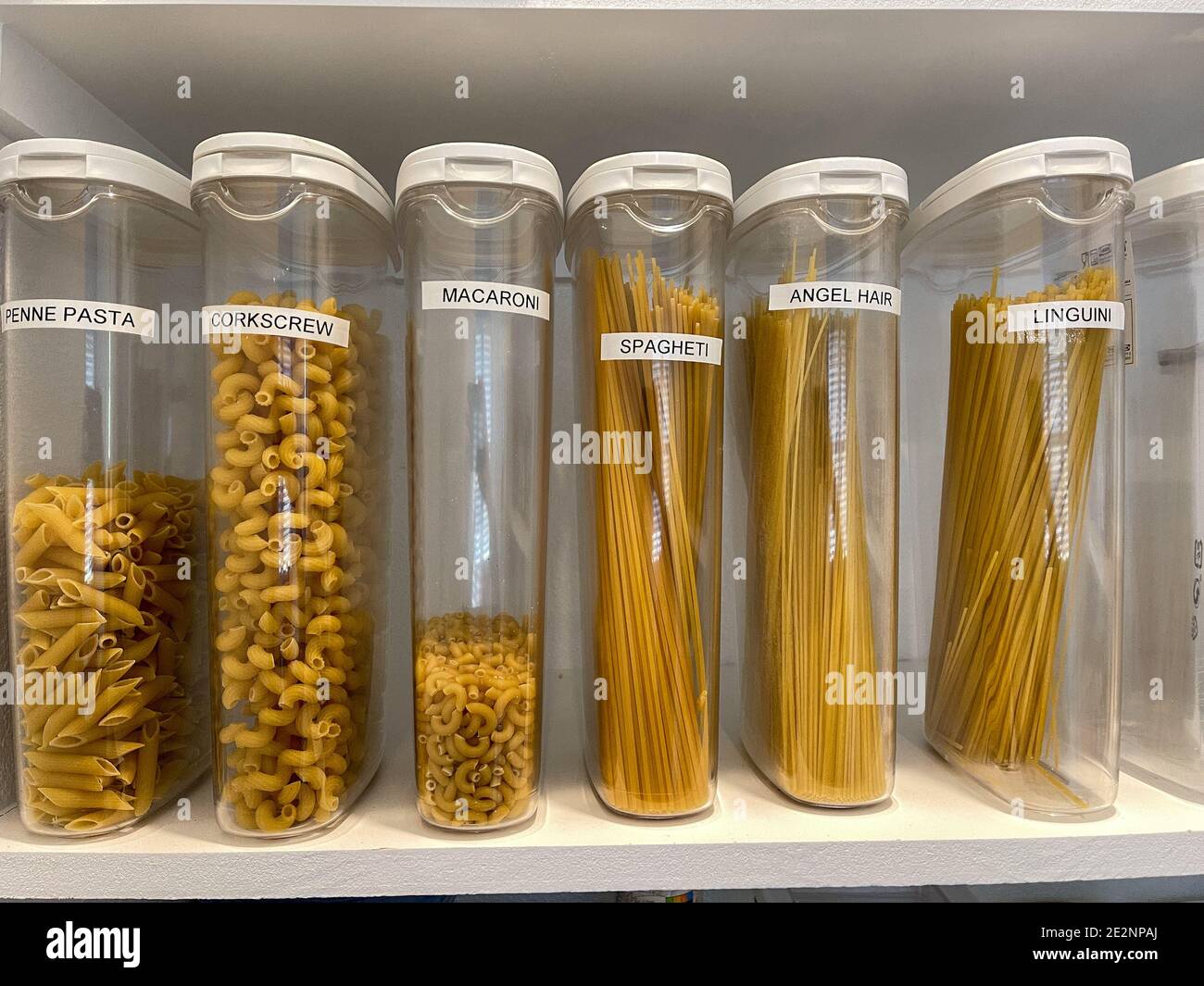 An organized pantry shelf with various types of pasta in plastic ...