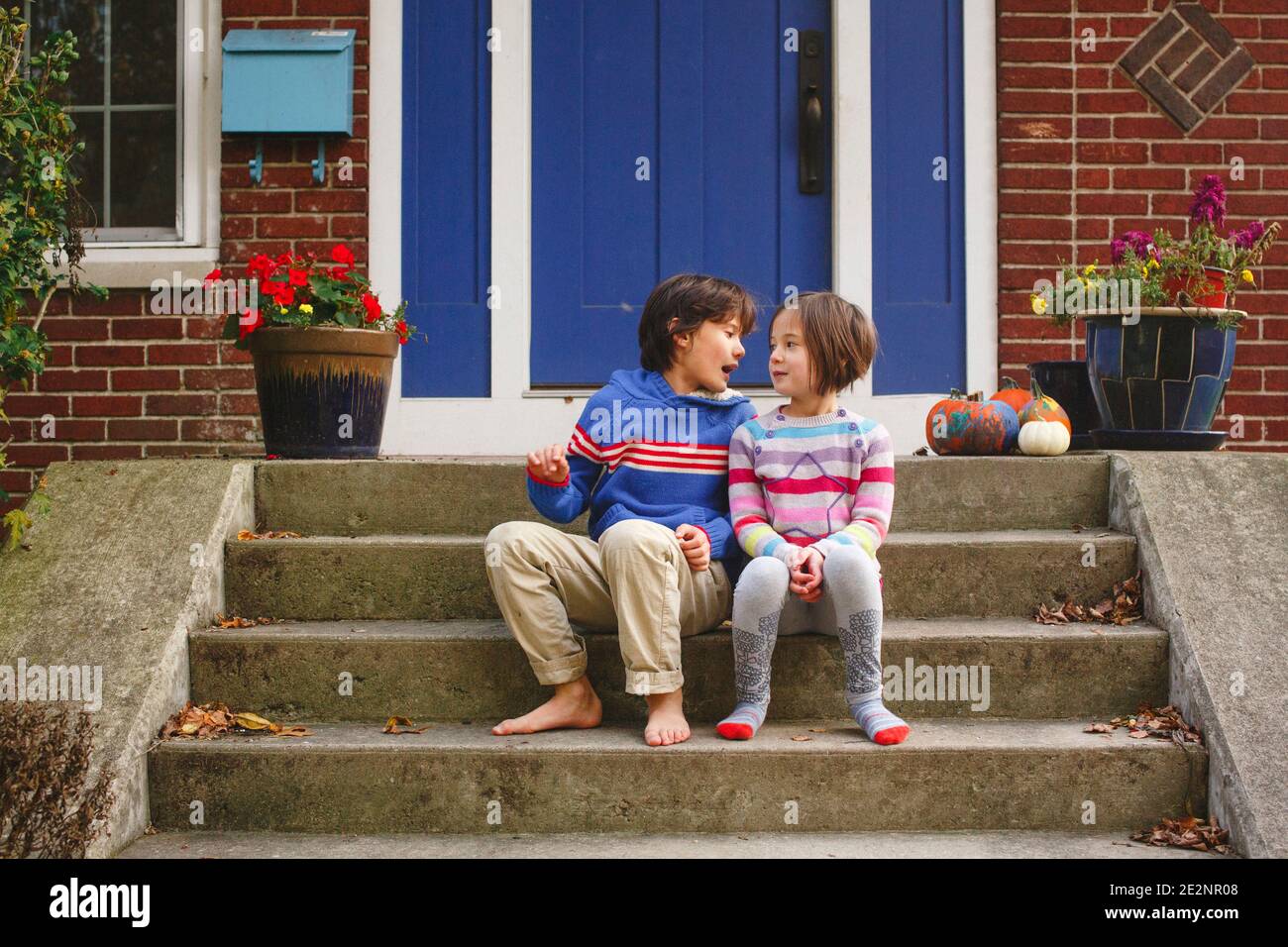 A brother and sister sit smiling together on front stoop of home Stock ...