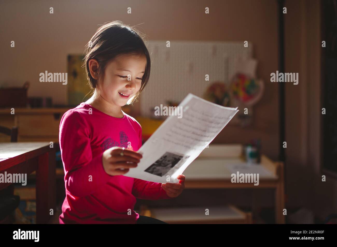 A smiling child in beautiful light studies a piece of paper, reading ...
