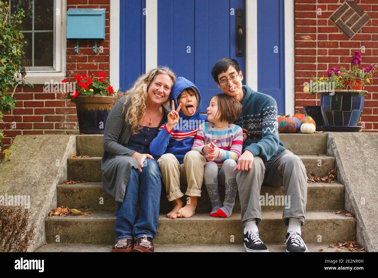 A happy family sit together on the front stoop of their home smiling ...