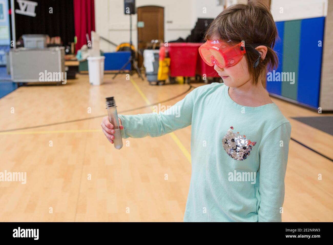 A cute little girl with safety goggles carefully observes a test tube ...