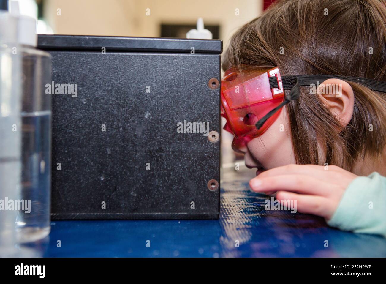 A little girl wearing safety goggles peers into a black box Stock Photo ...