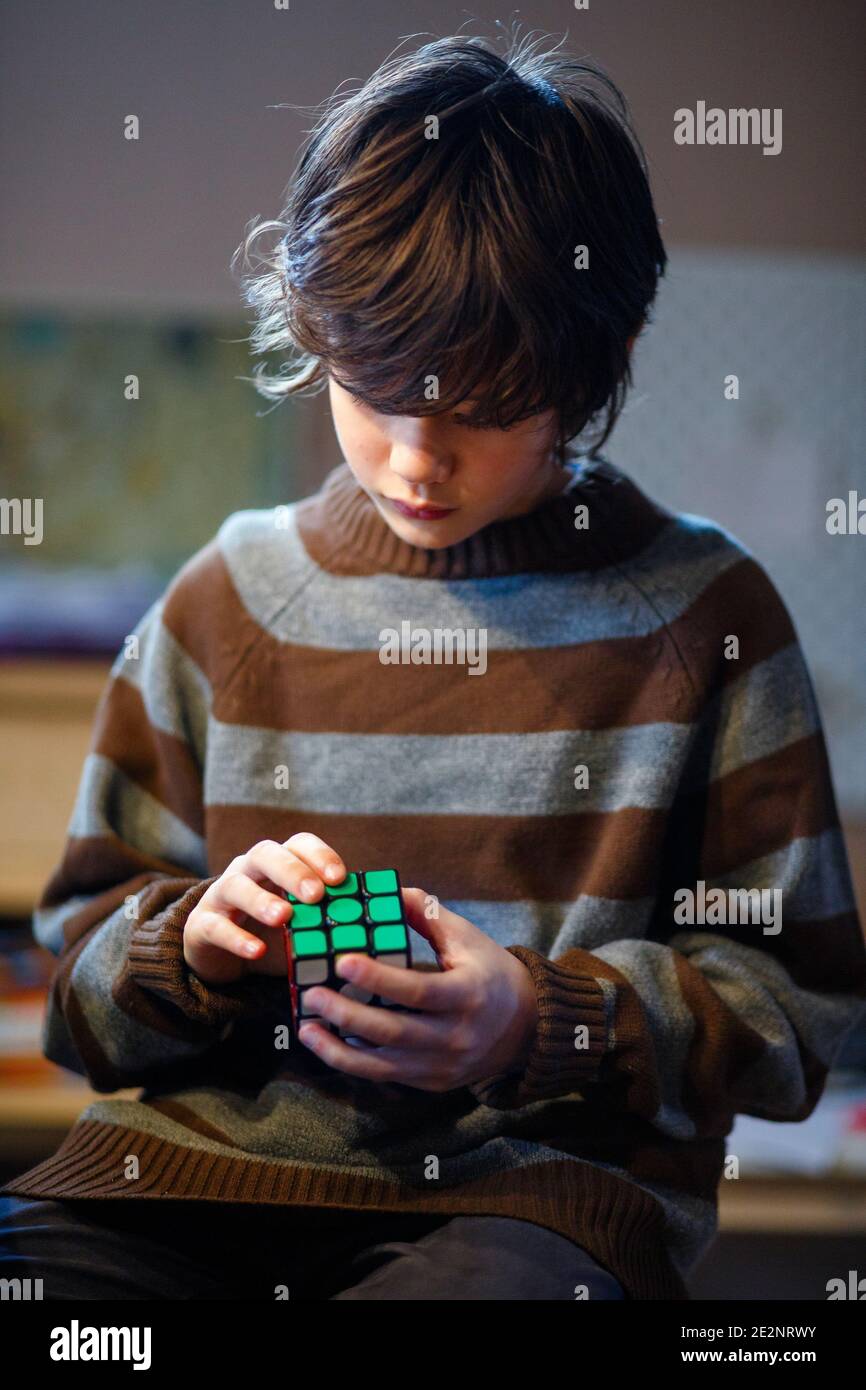 A small boy in oversize sweater patiently solves a Rubik's cube Stock ...