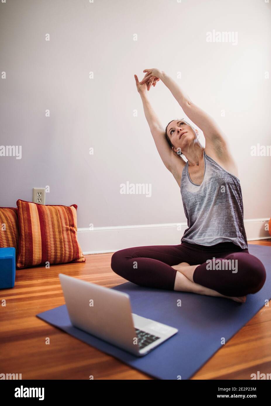 woman sits on yoga mat in front of laptop computer and stretches Stock ...