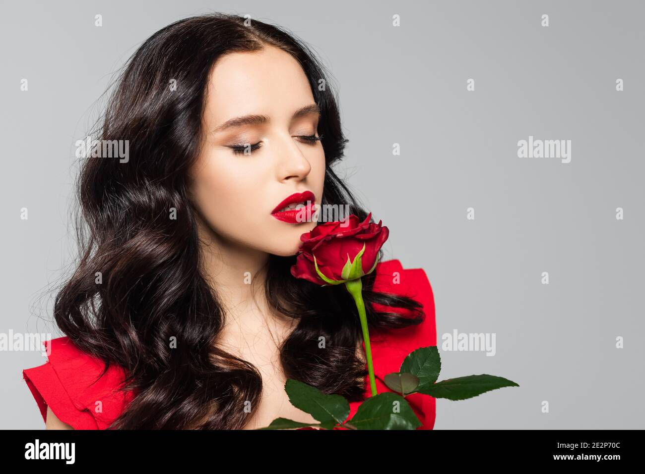 brunette young woman smelling red rose isolated on grey Stock Photo - Alamy