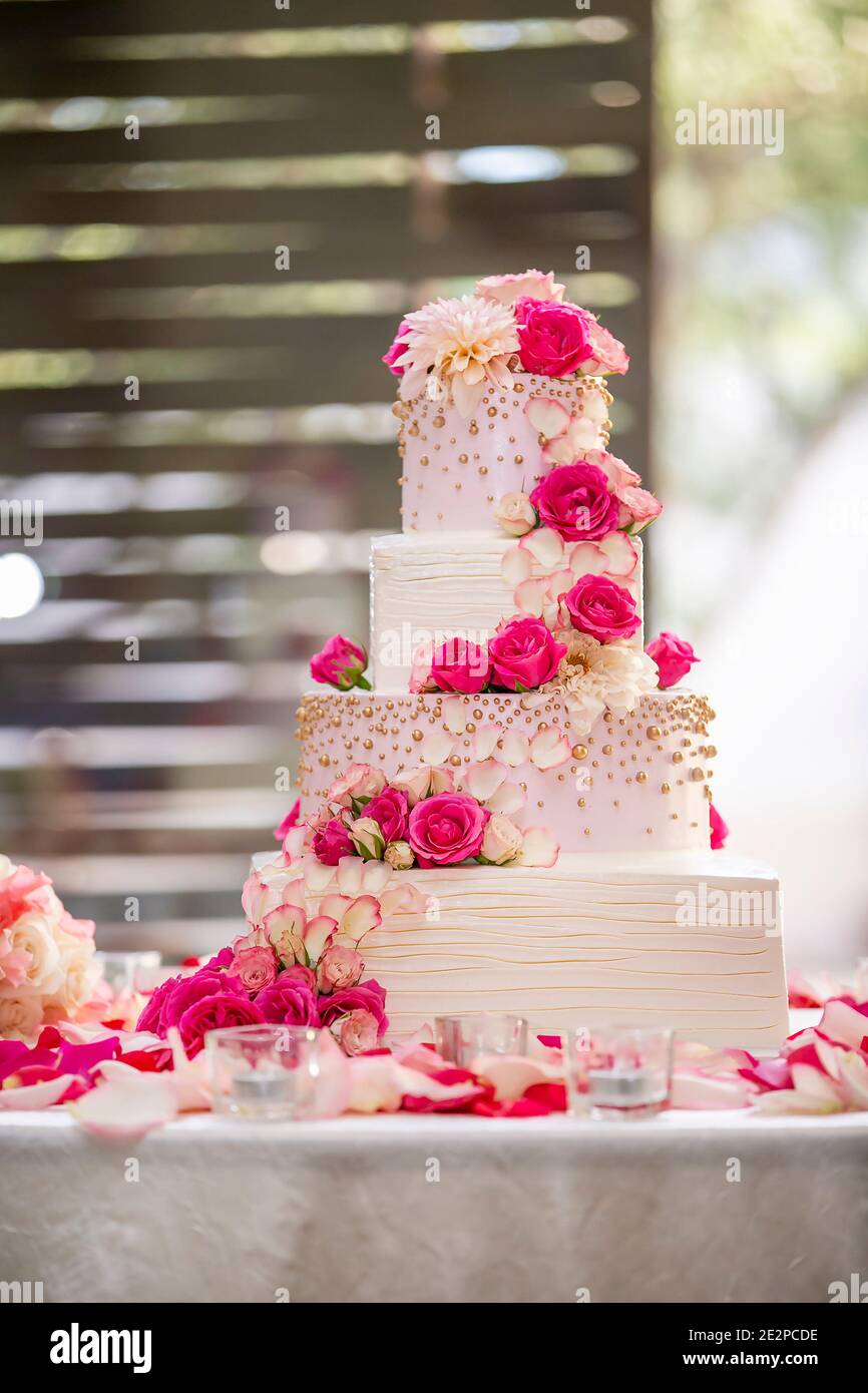 White frosting four tiered wedding cake decorated with pink roses on a ...