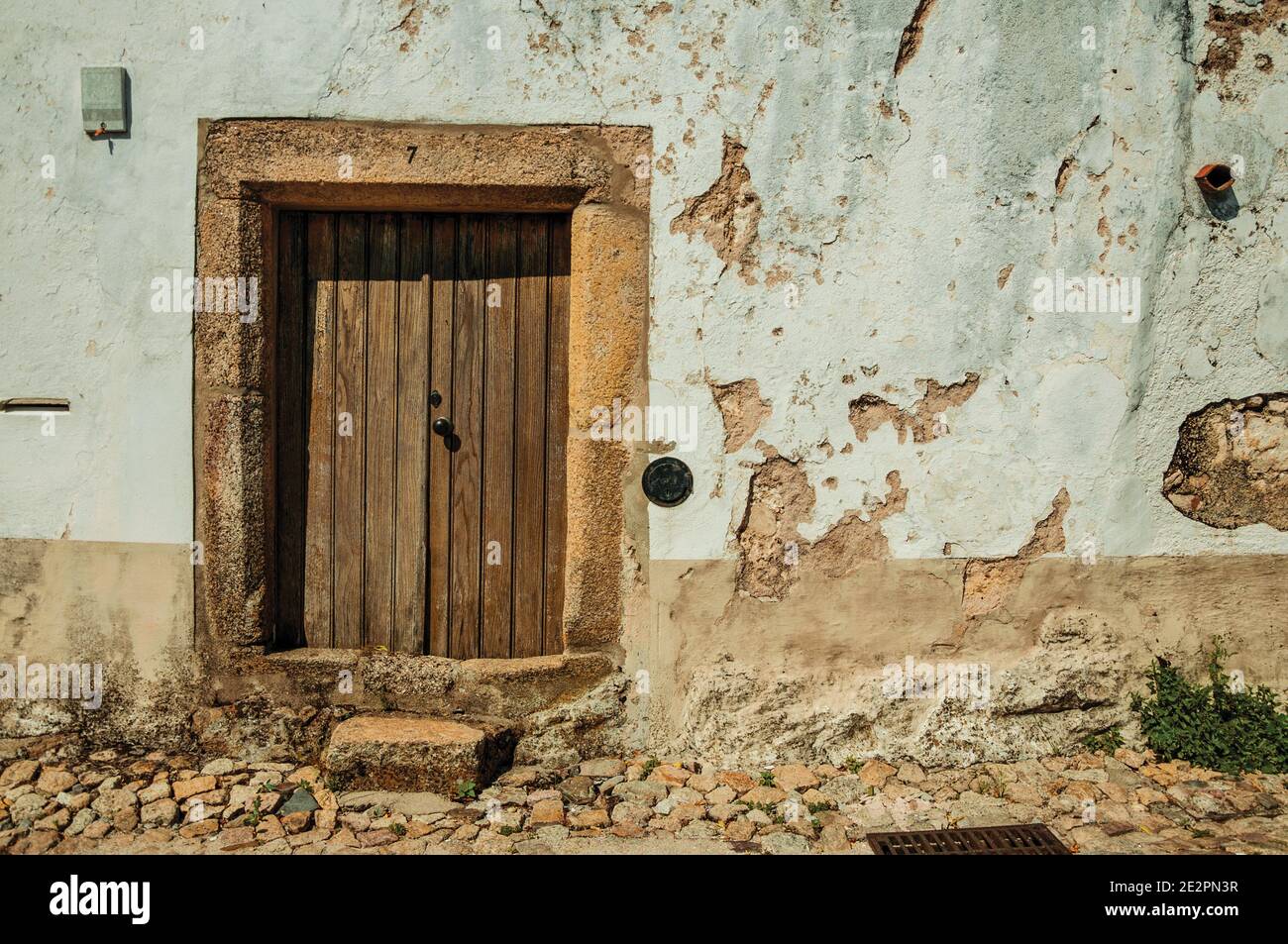 Old house with worn plaster wall and wooden door in cobblestone alley ...