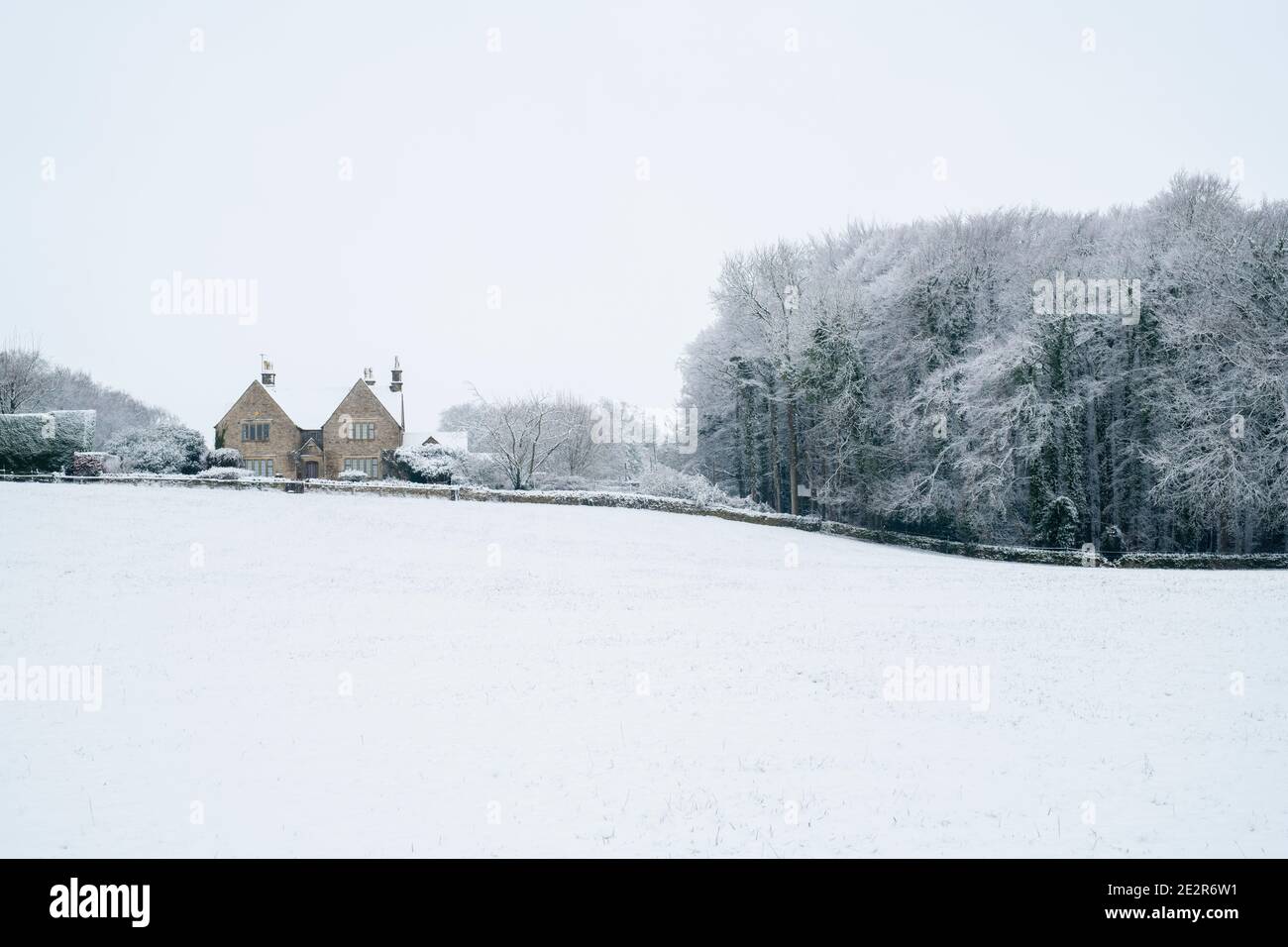 Cotswold stone house, trees and field in the december snow in the ...