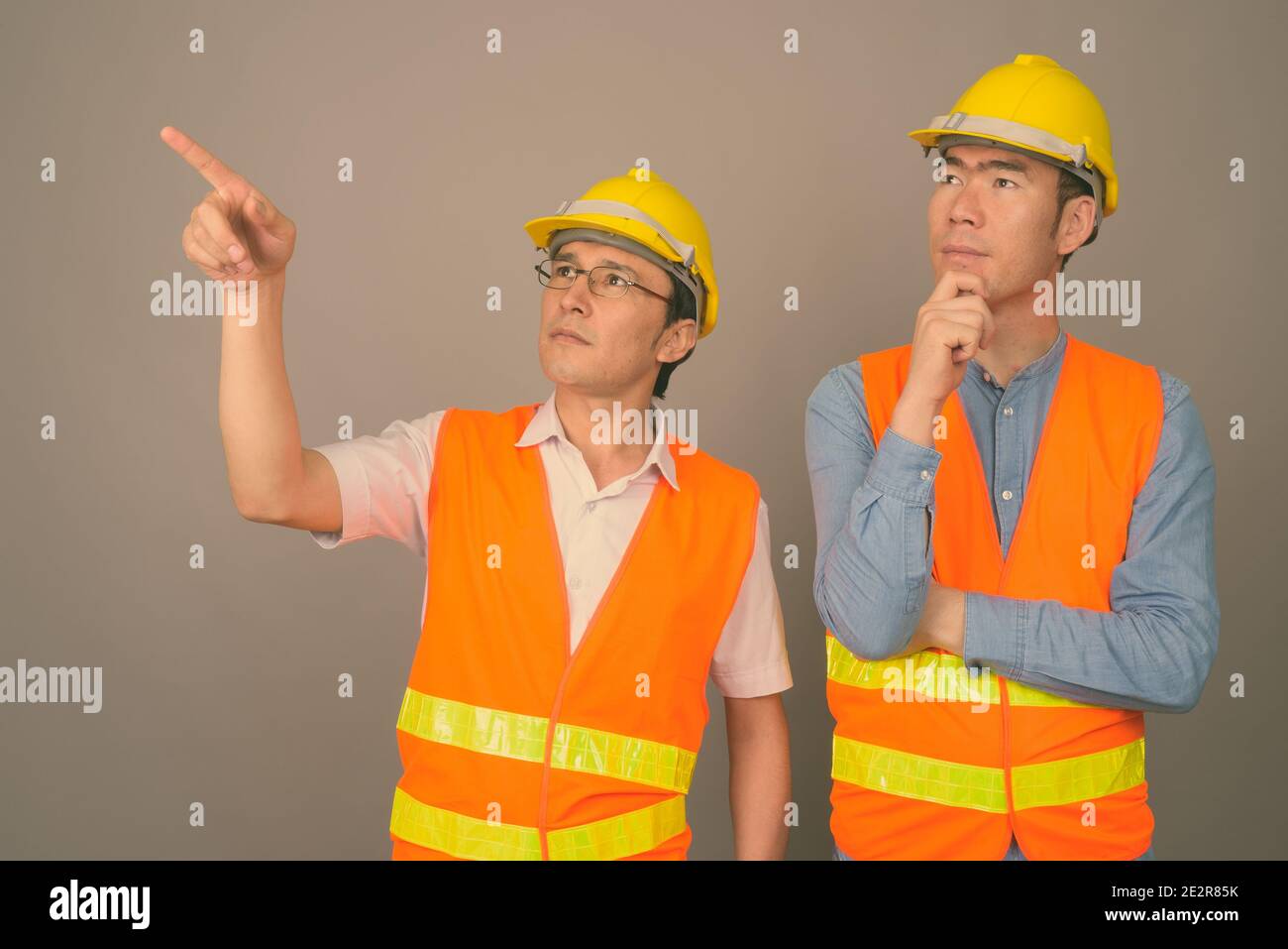 Two young Asian men construction worker together against gray ...