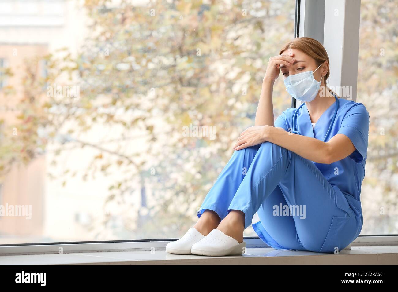 Sad female doctor sitting on window sill in clinic Stock Photo - Alamy