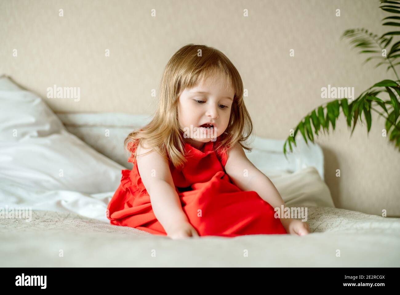 Smiling baby sitting on bed.Cute red-haired girl plays at home in a ...