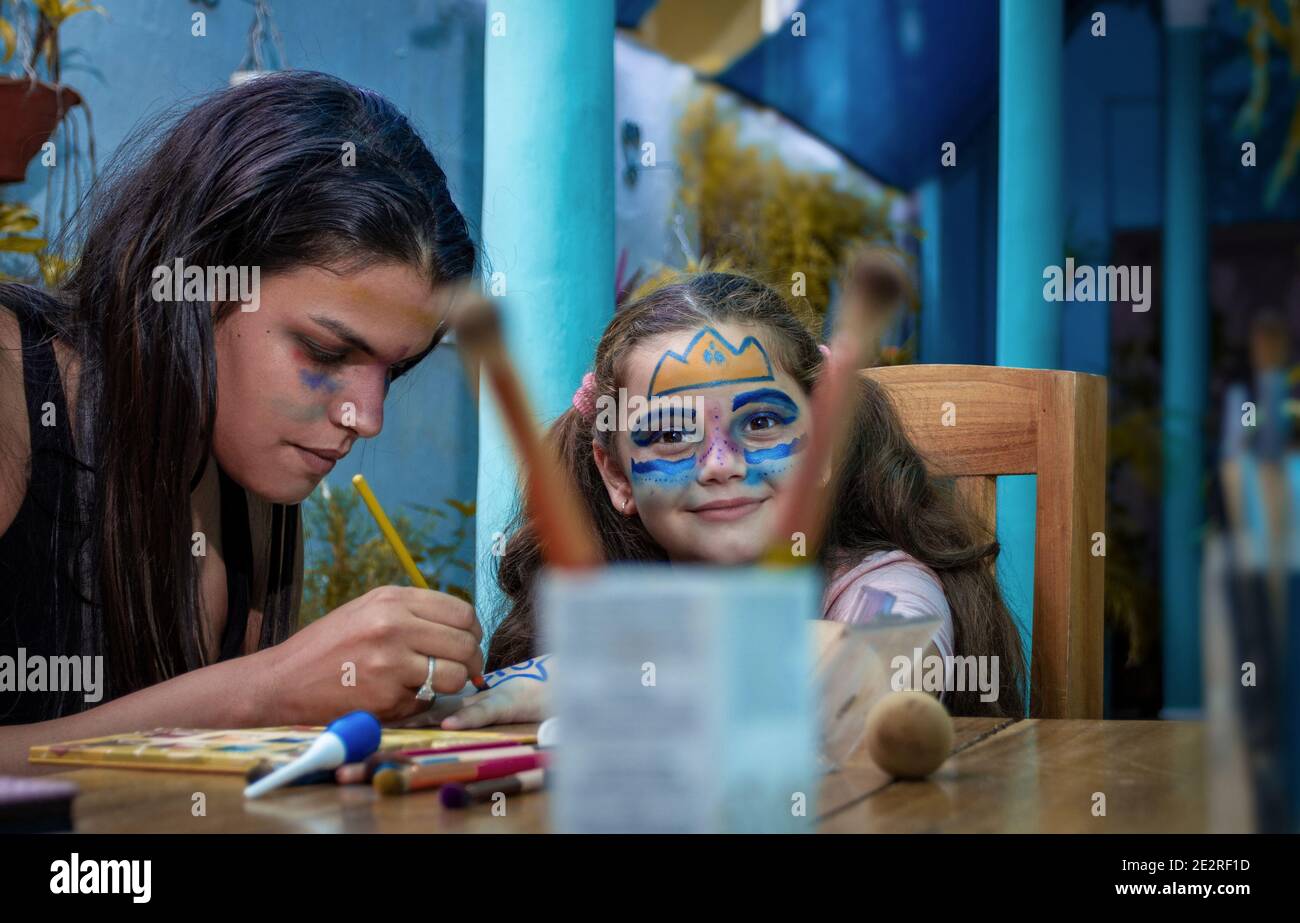 Girl with drawings on her face looking straight ahead while a young ...