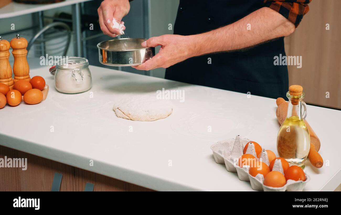 Senior man sifting flour with metallic sieve over dough. Happy elderly ...