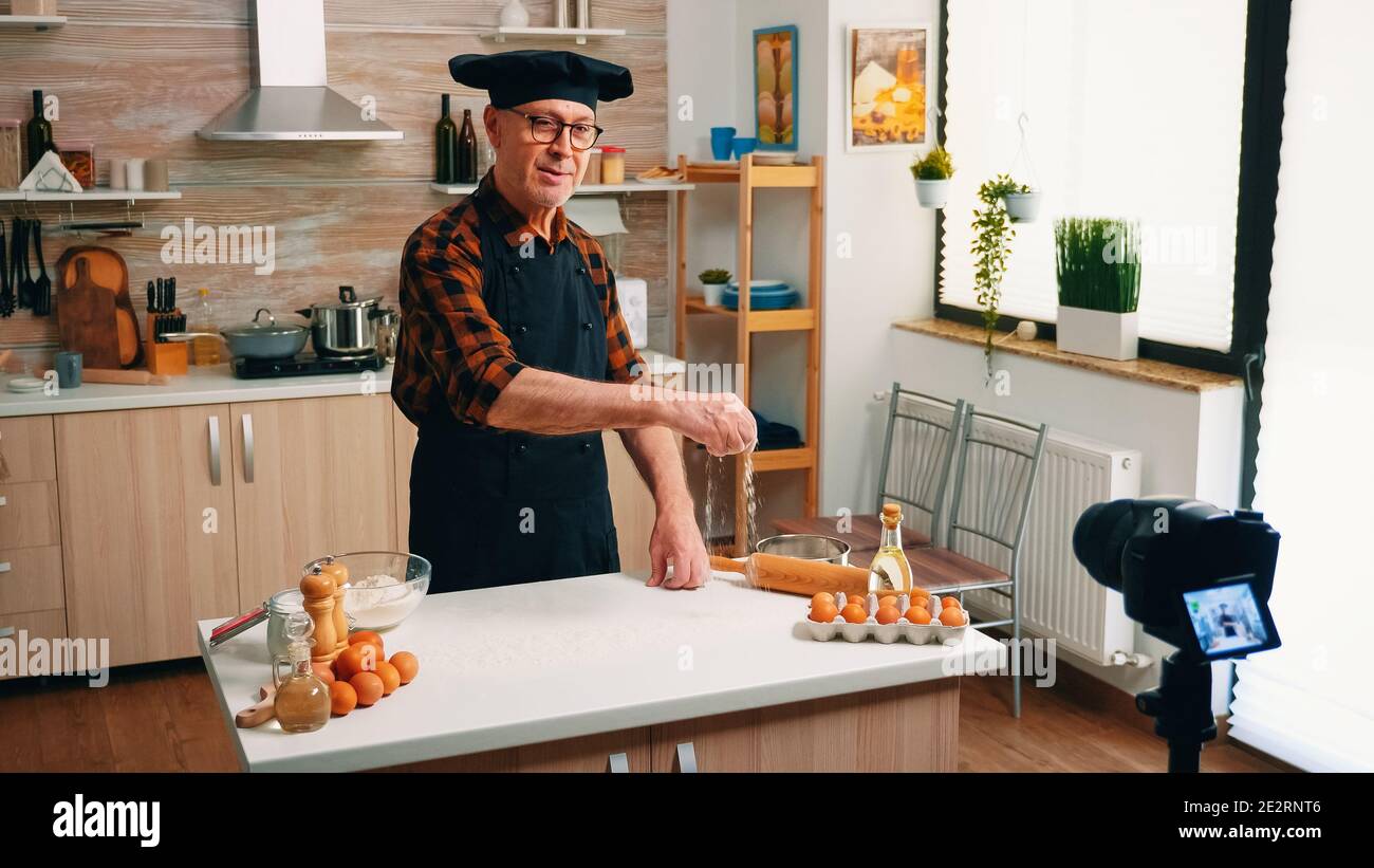 Old man shooting culinary video using camera on tripod in the kitchen ...