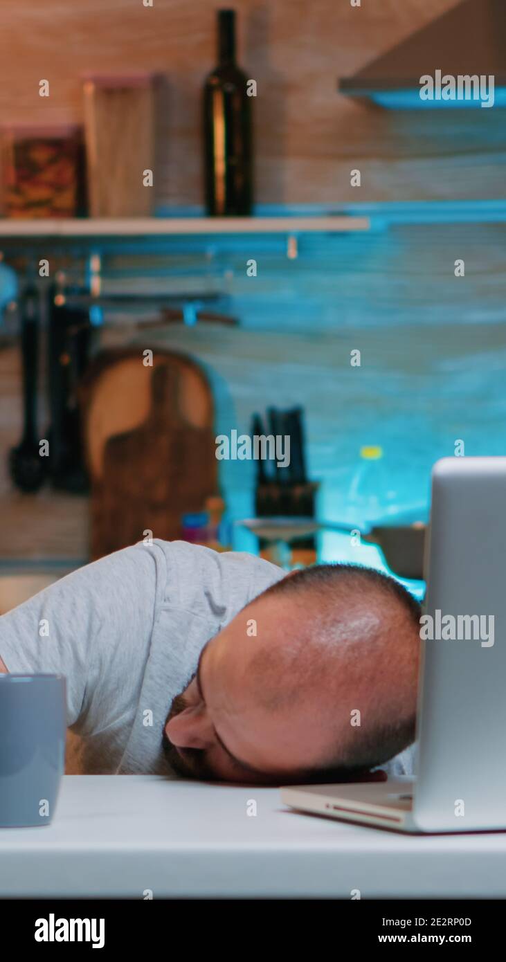 Overworked man sleeping on kitchen desk working remotely late hours at ...