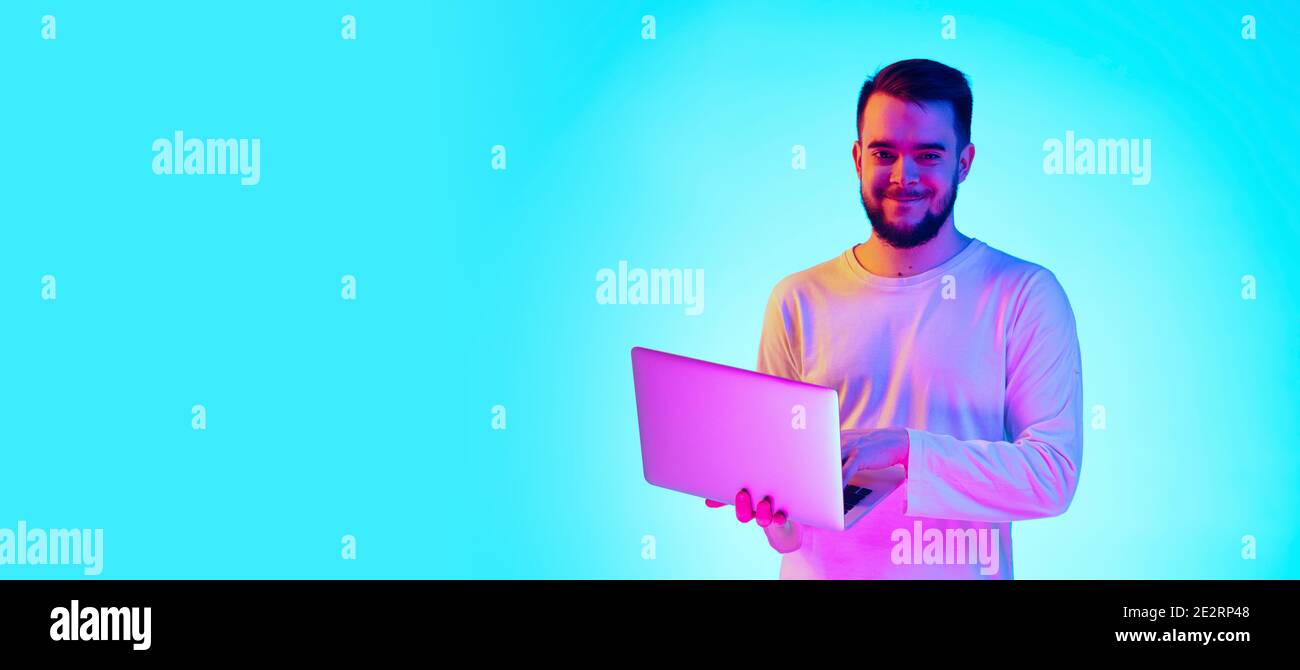 Using laptop. Caucasian man's portrait with device on blue studio ...