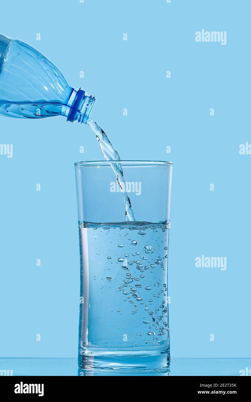 Pouring clean drinking water from blue plastic bottle into glass on ...