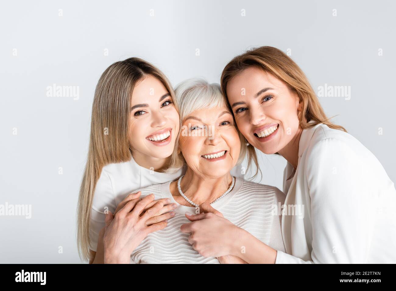 three generation of positive women smiling while looking at camera and ...