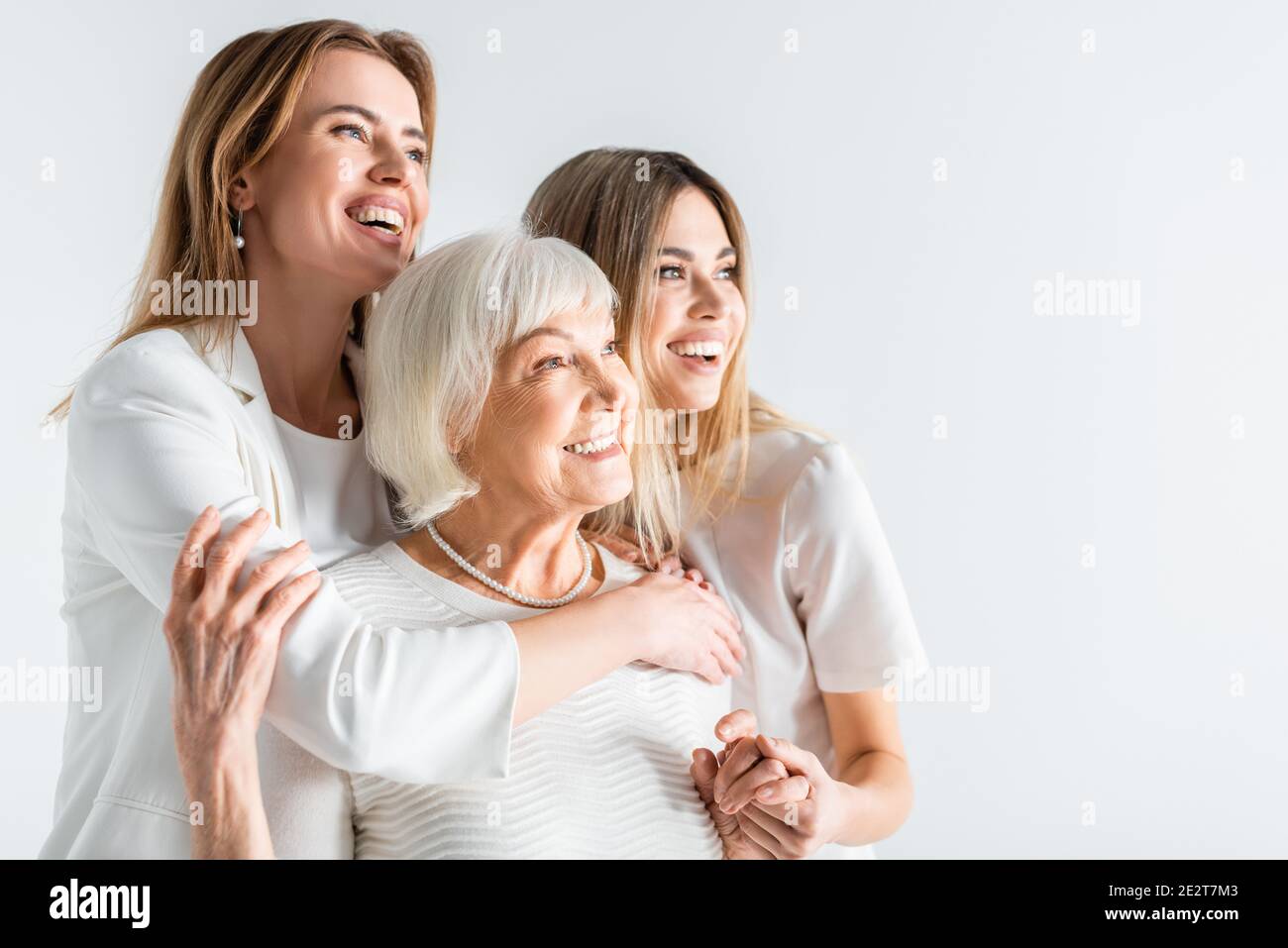 three generation of positive women smiling while hugging isolated on ...