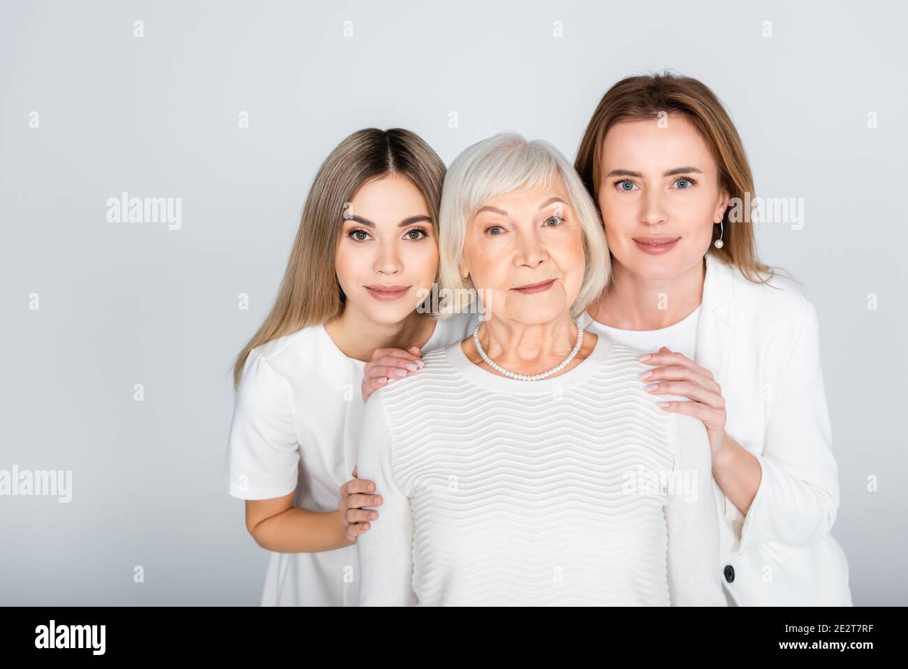 three generation of women smiling while looking at camera isolated on ...