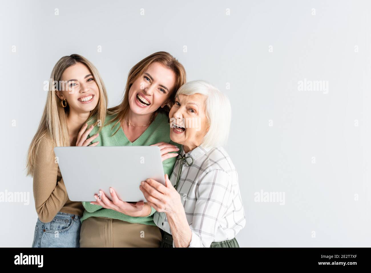 three generation of joyful women looking at camera near laptop isolated ...