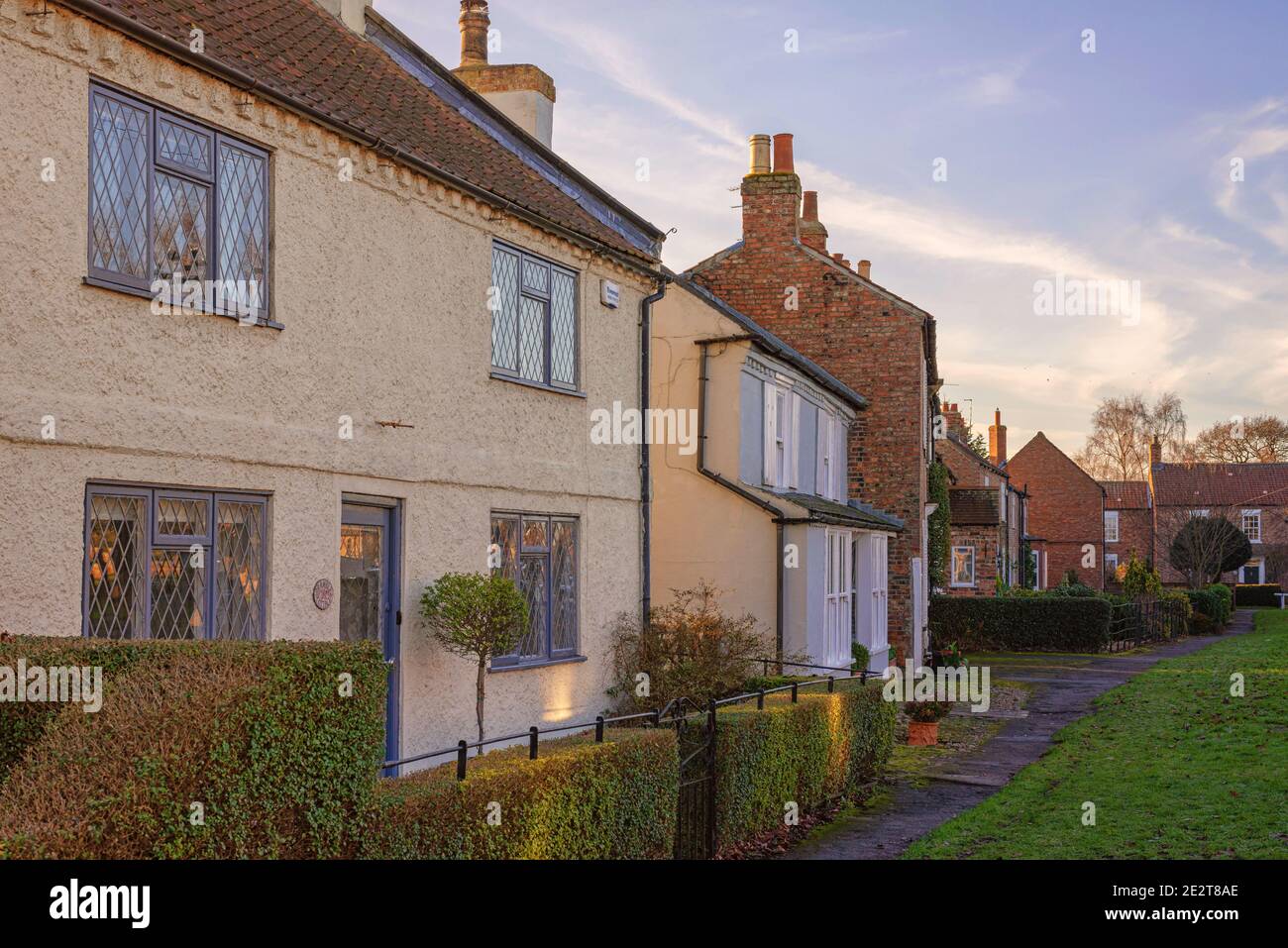 A row of cottages in a village setting. A trimmed hedge surrounds a ...