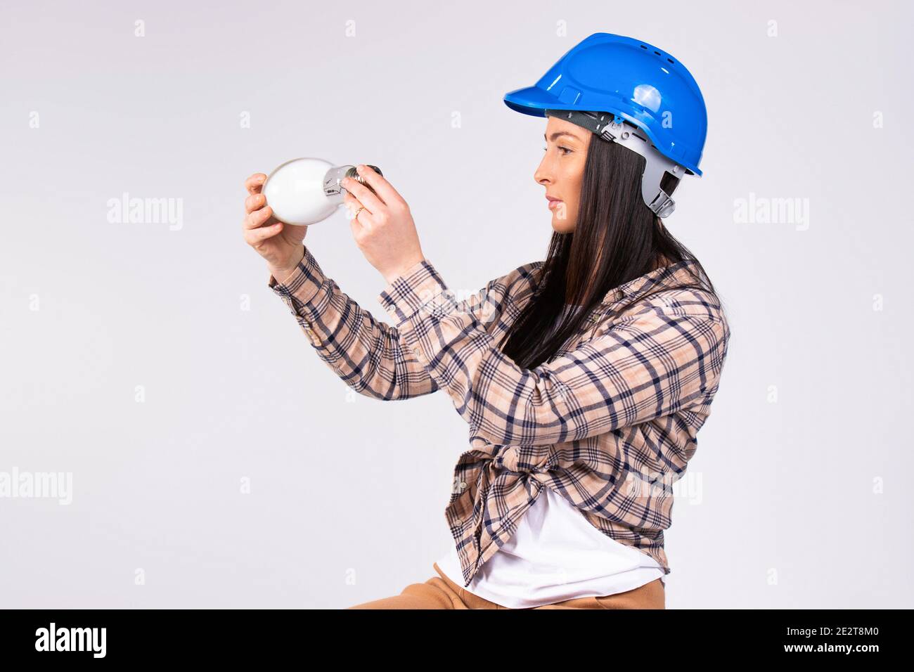 An electrician woman examines a LED lamp in her hands on a white ...
