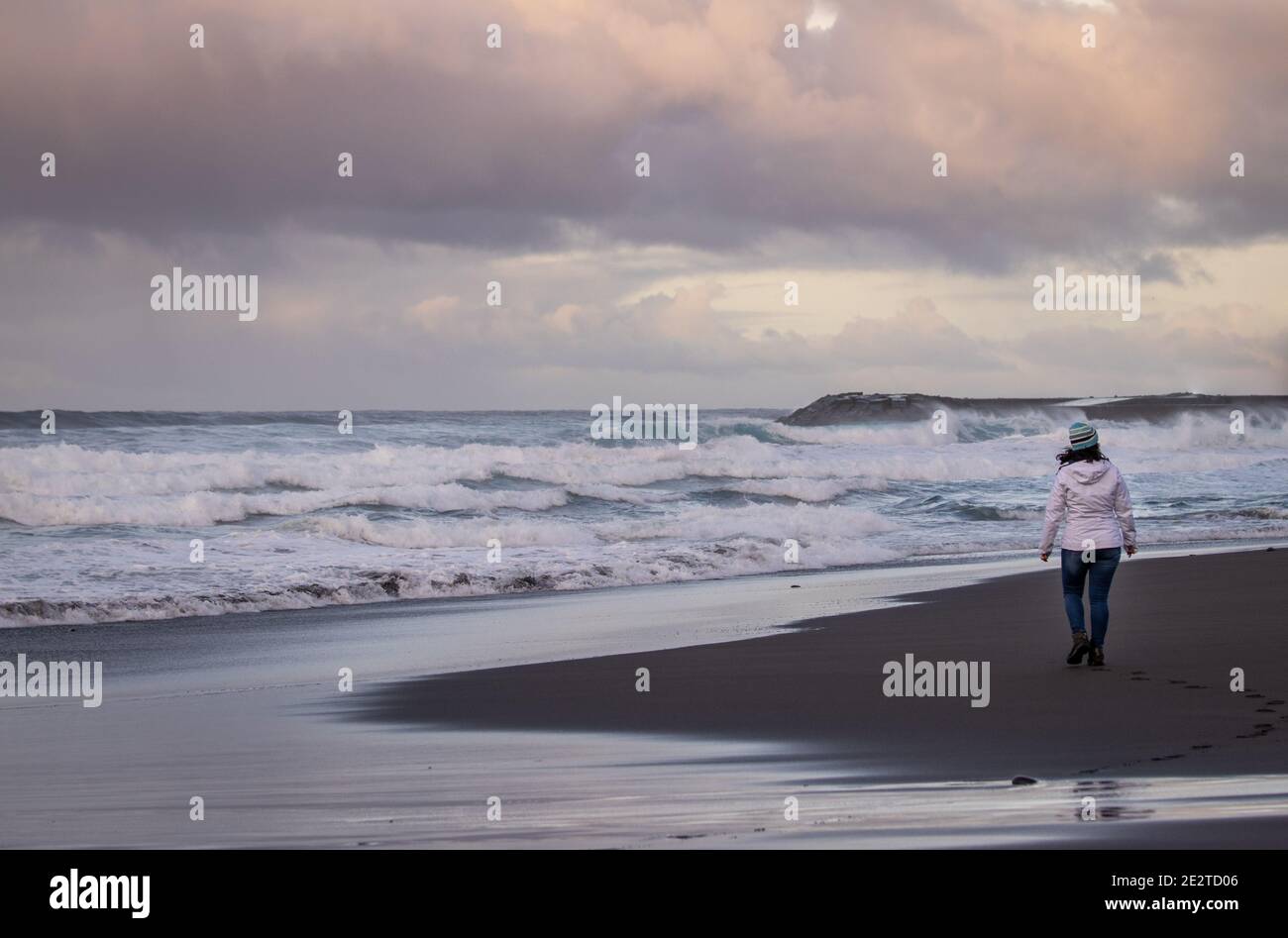 Young woman by the atlantic ocean, walking, waves crashing in ...