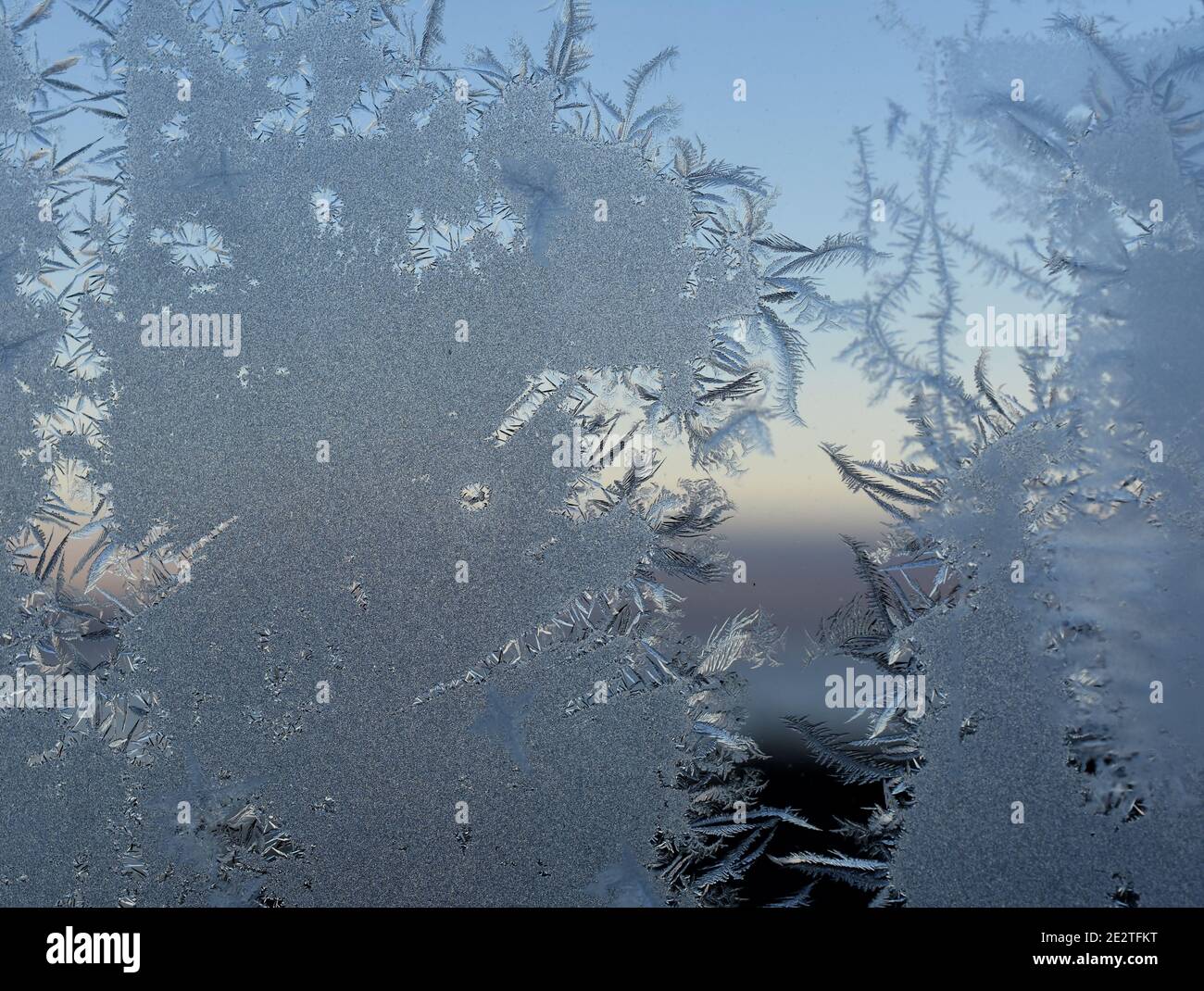 Frost pattern on window with glimpse of sunset outdoor behind crystals ...