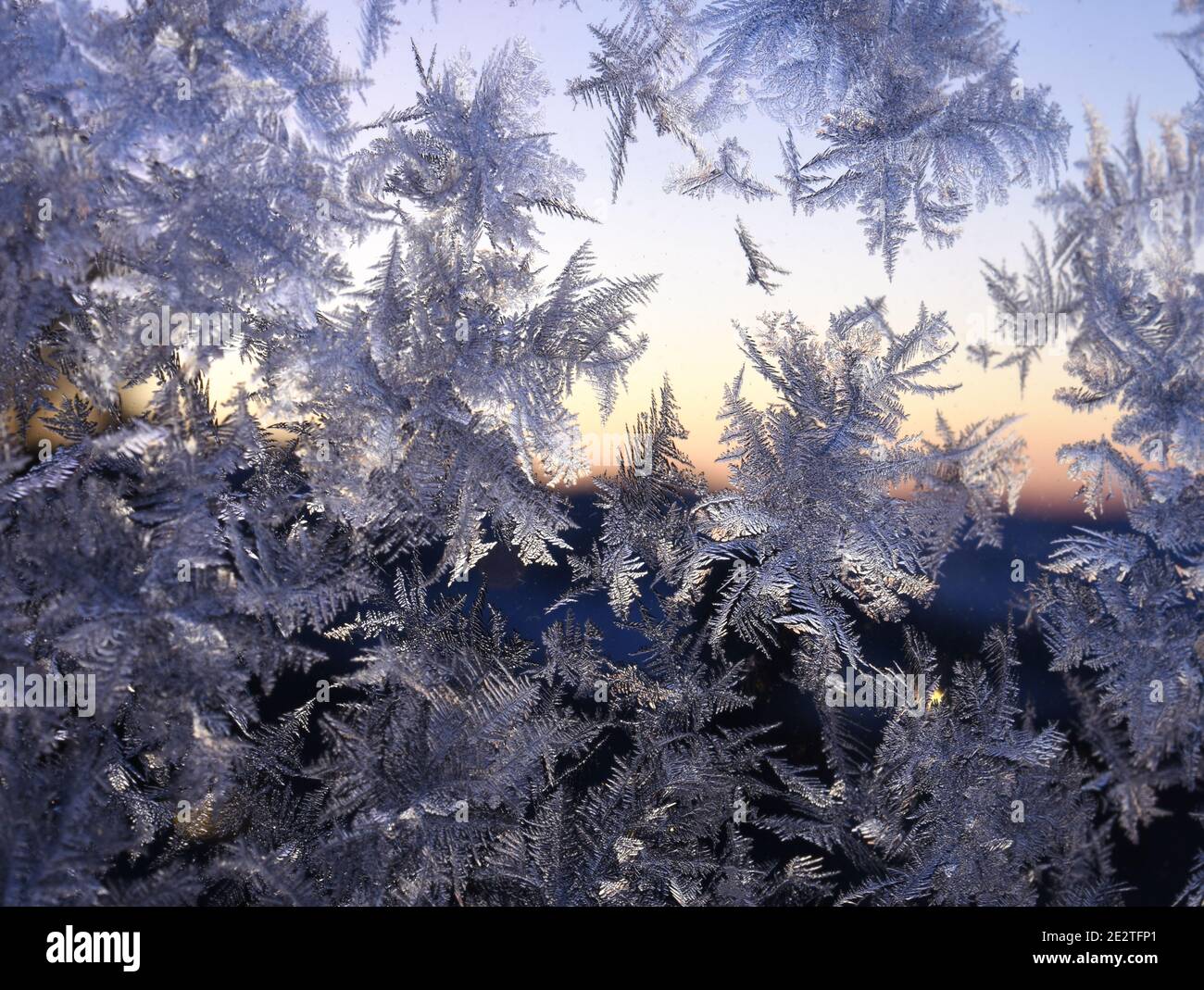 Frost pattern on window with glimpse of sunset outdoor behind crystals ...