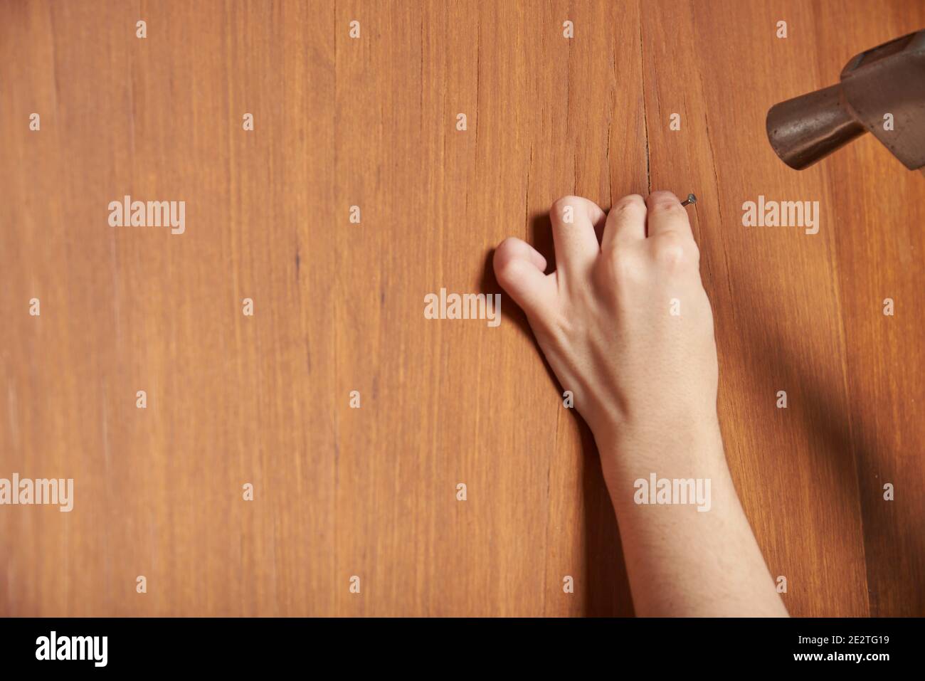 Young woman driving a nail into a wooden surface using a hammer ...