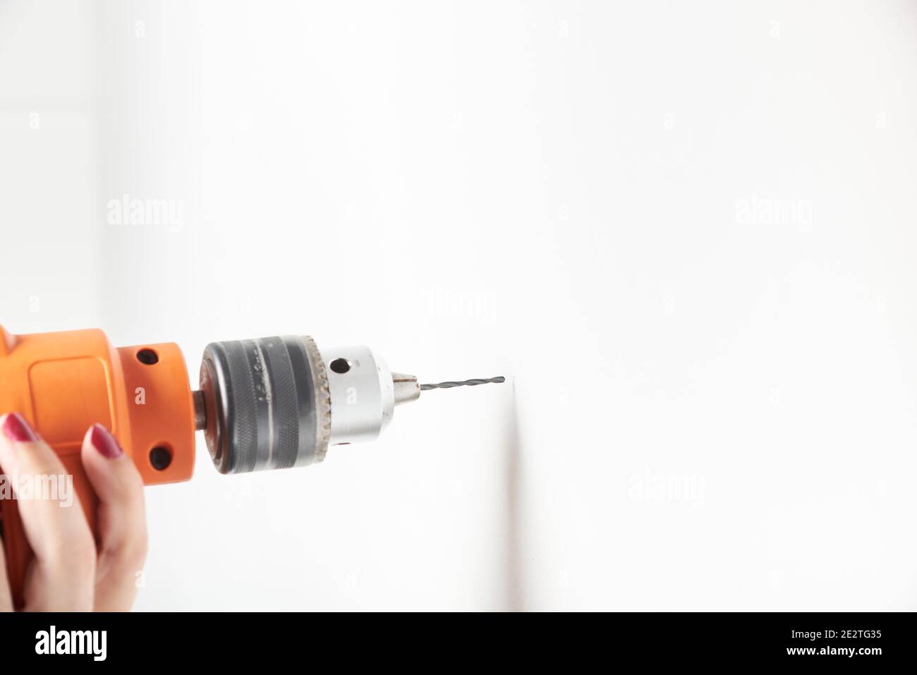 Woman with a power drill drilling a white wall. Detail image with copy ...