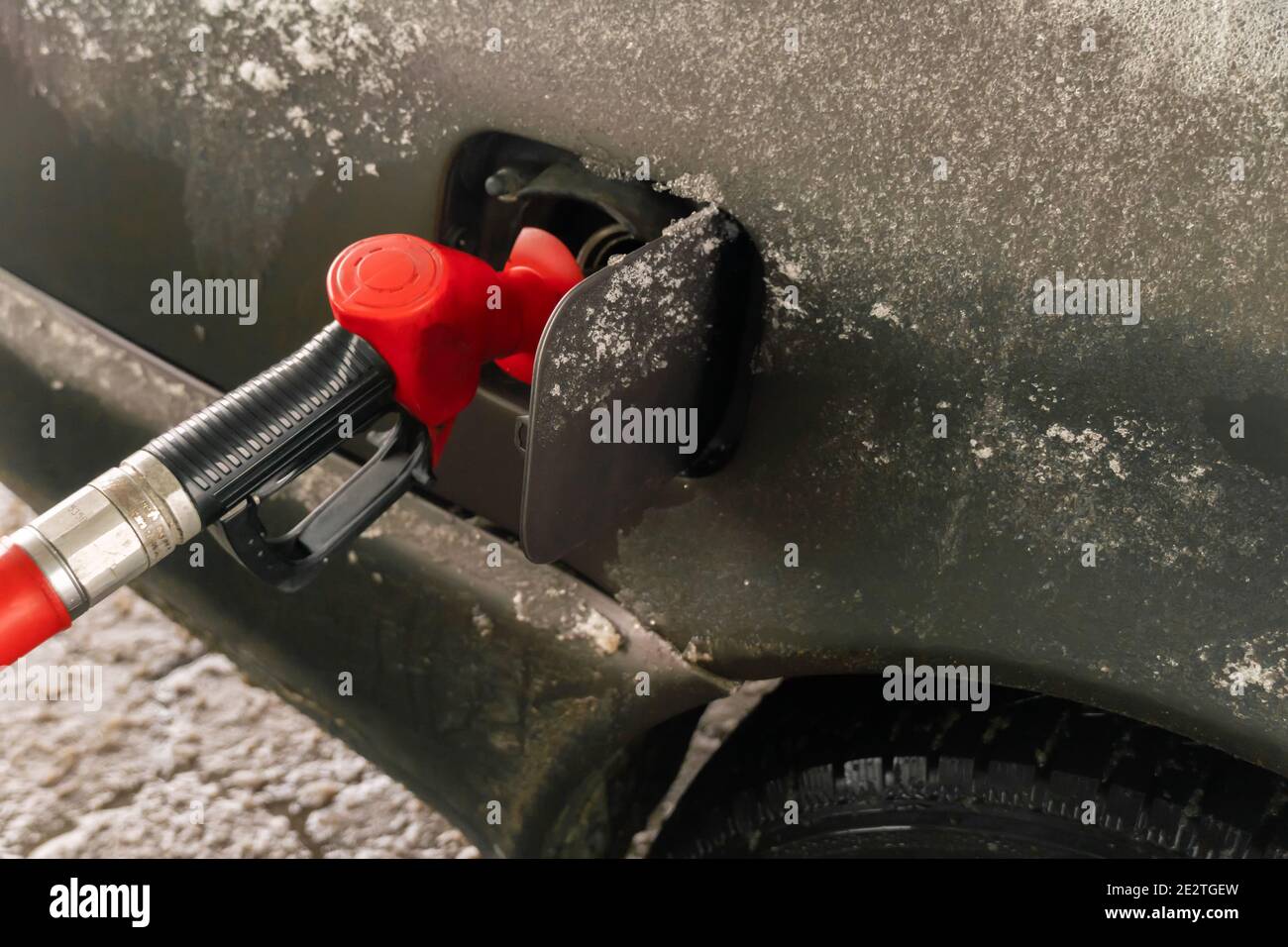 Red refueling gun in the fuel tank of a dirty, snowy car at a gas ...